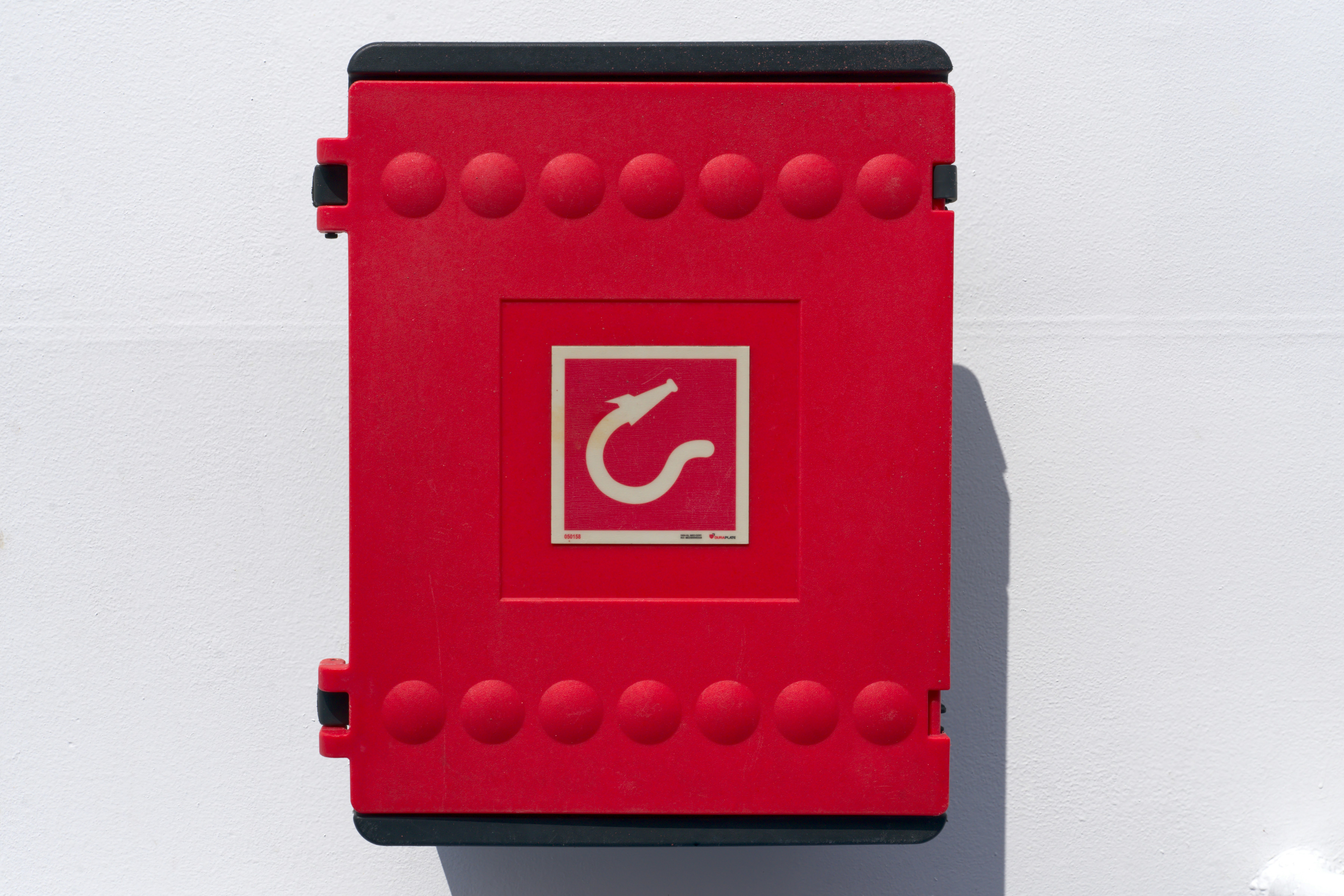Red utility box on stark white wall with shadow