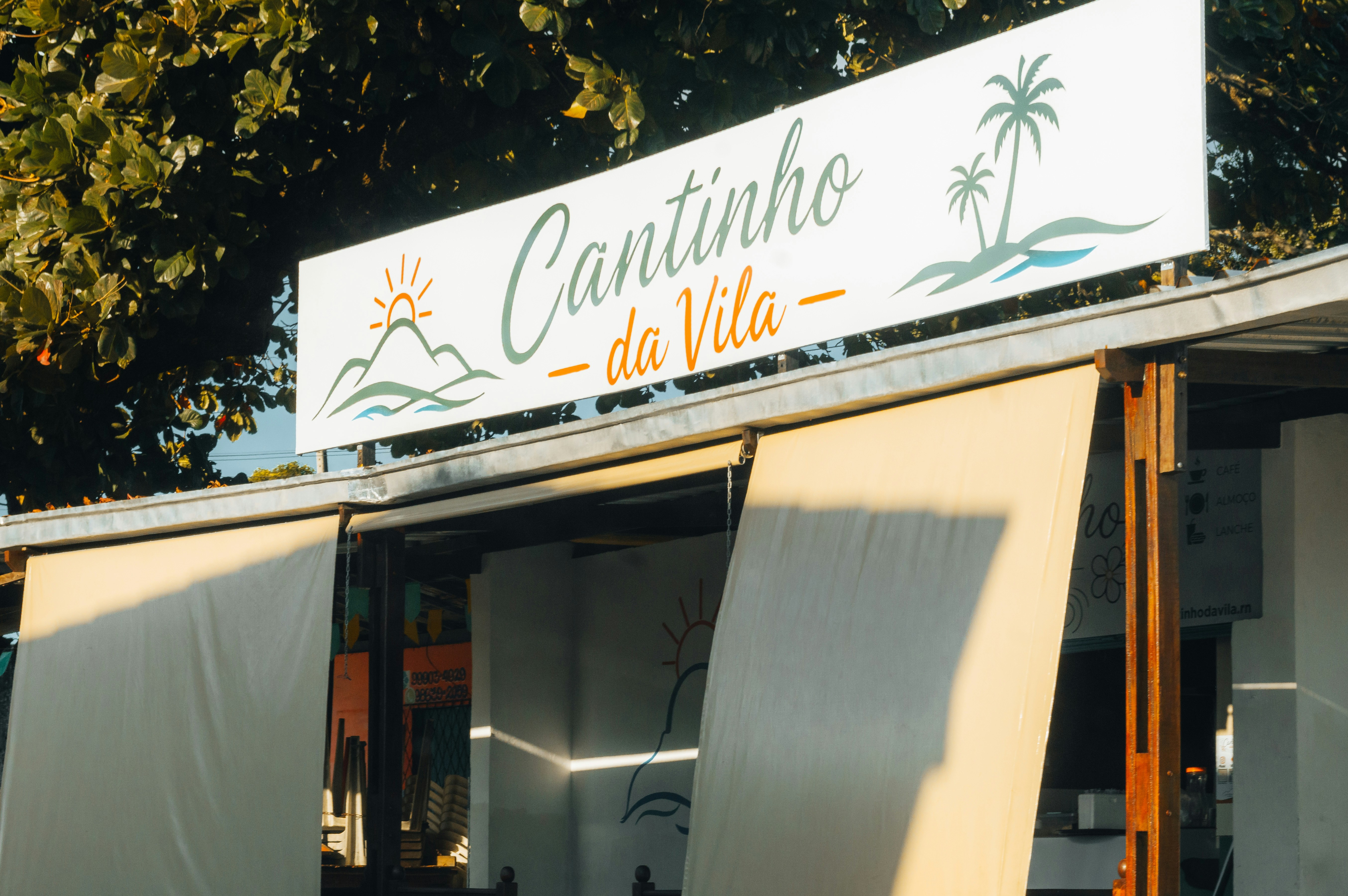 Cantinho da Vila: A Sunlit Café Sign Above Open Awnings