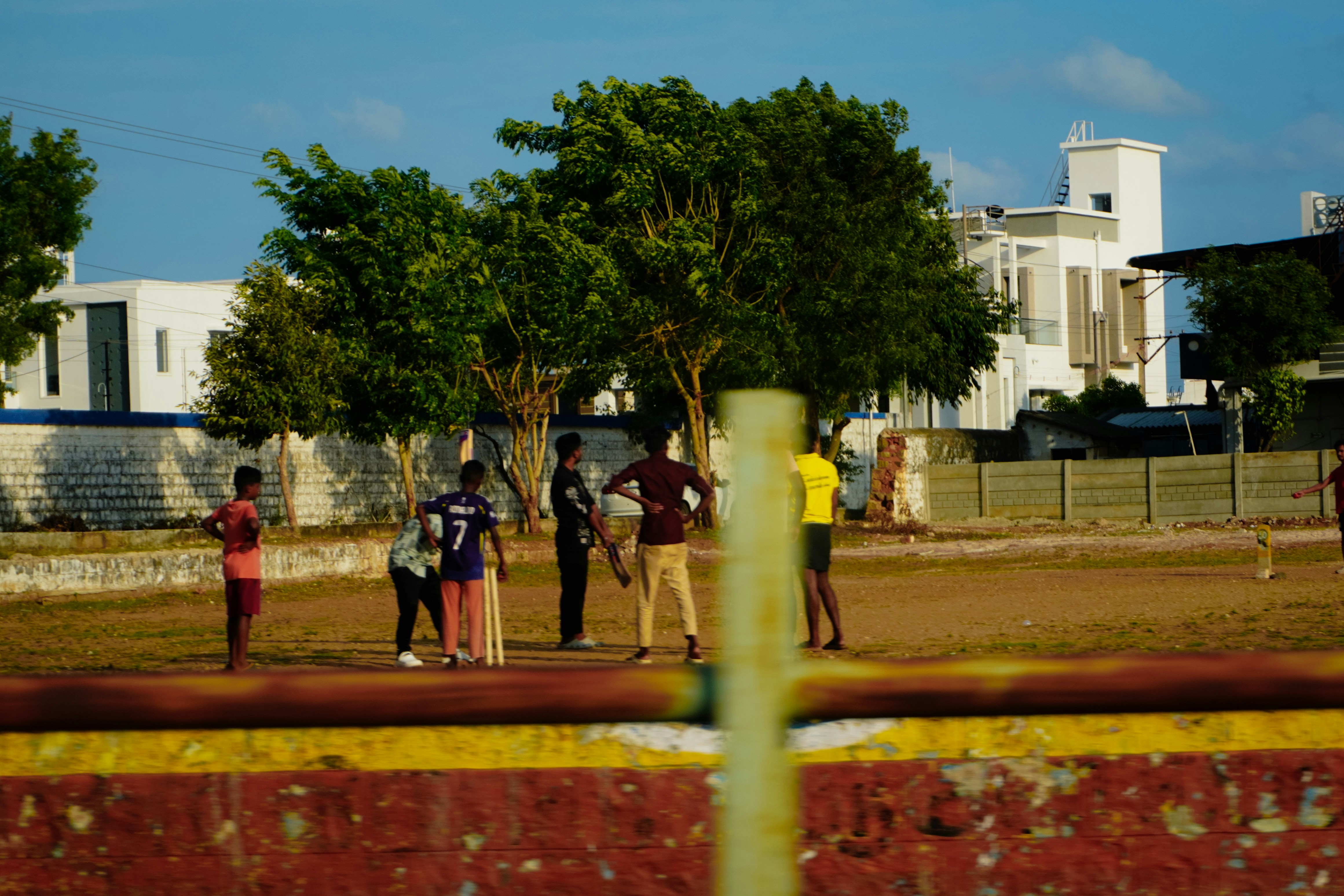 Group of kids and adults in a sunlit yard behind a weathered red wall
