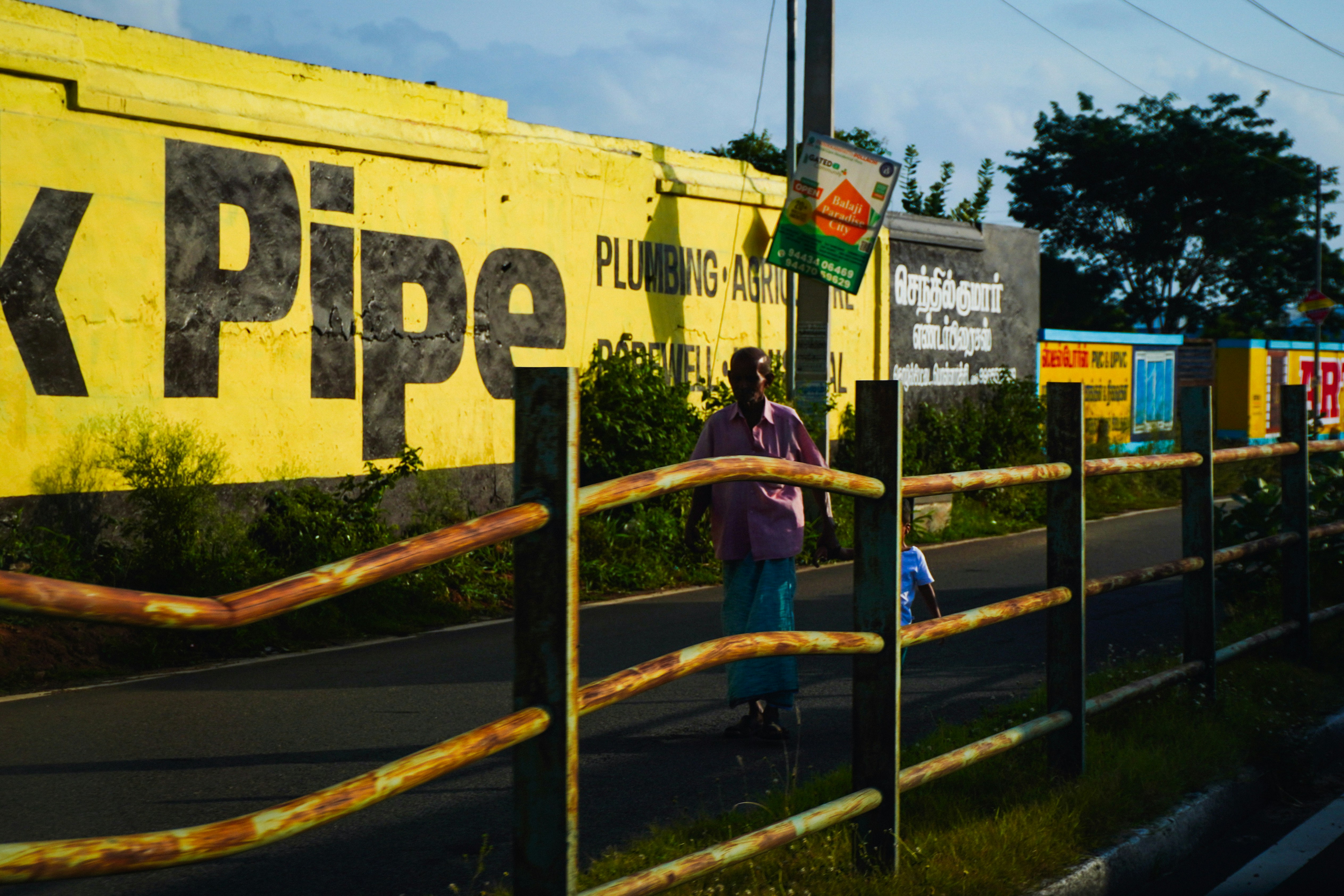 Man in purple shirt and child by yellow wall with signage and wooden fence