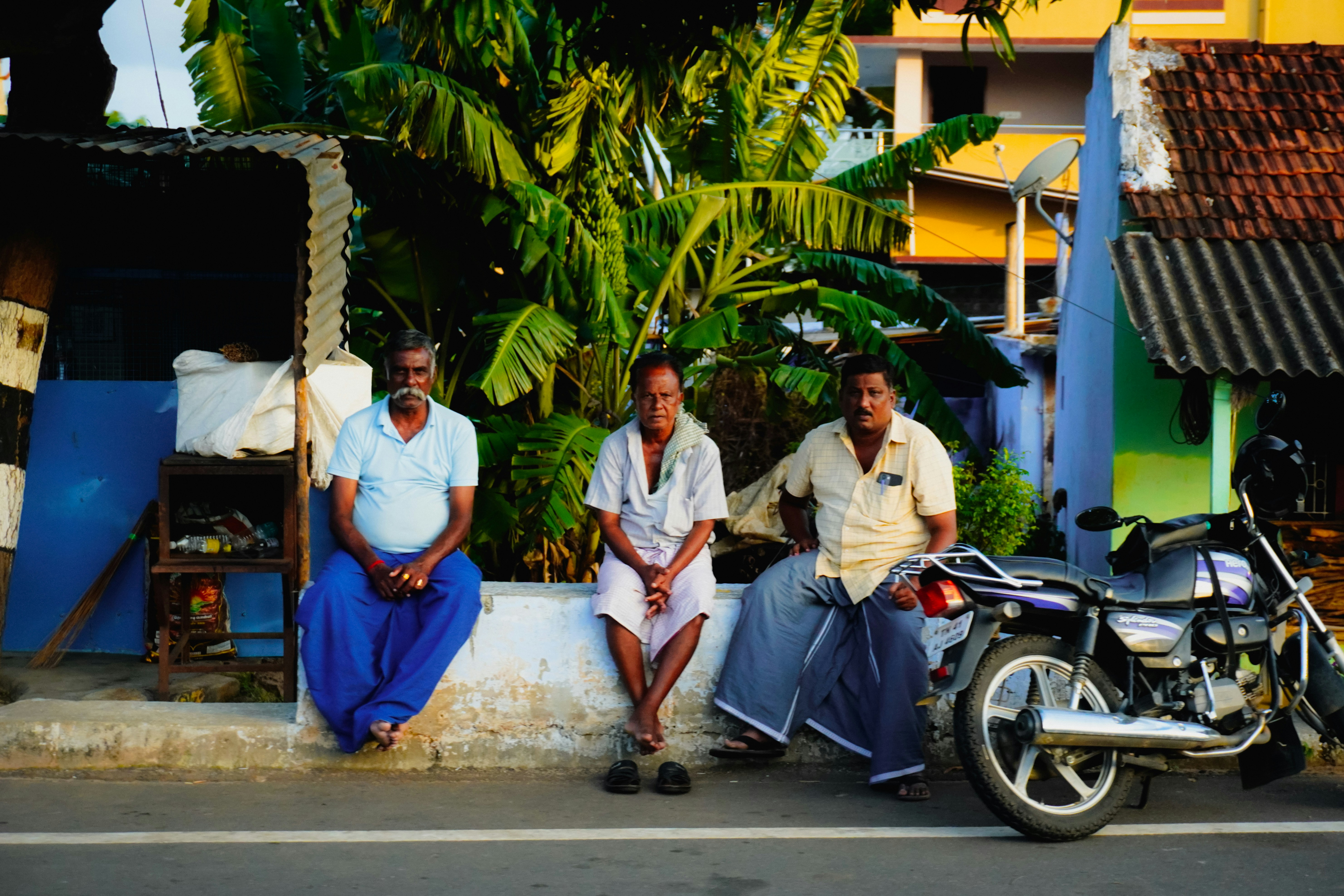 Three Gentlemen and a Motorcycle: Street Calm by a Banana Leaf Wall