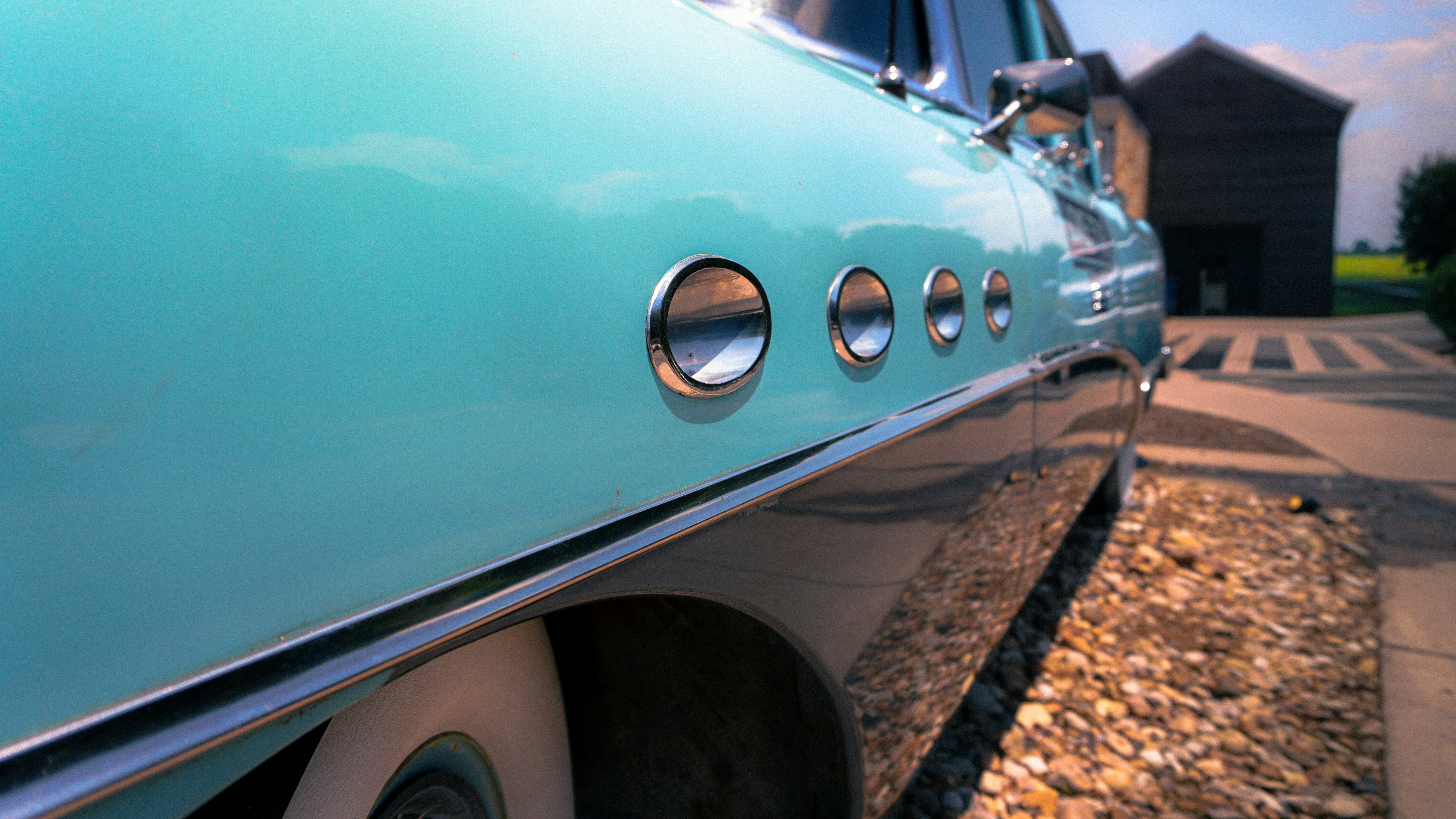 Gleaming teal vintage car with chrome fender portholes.