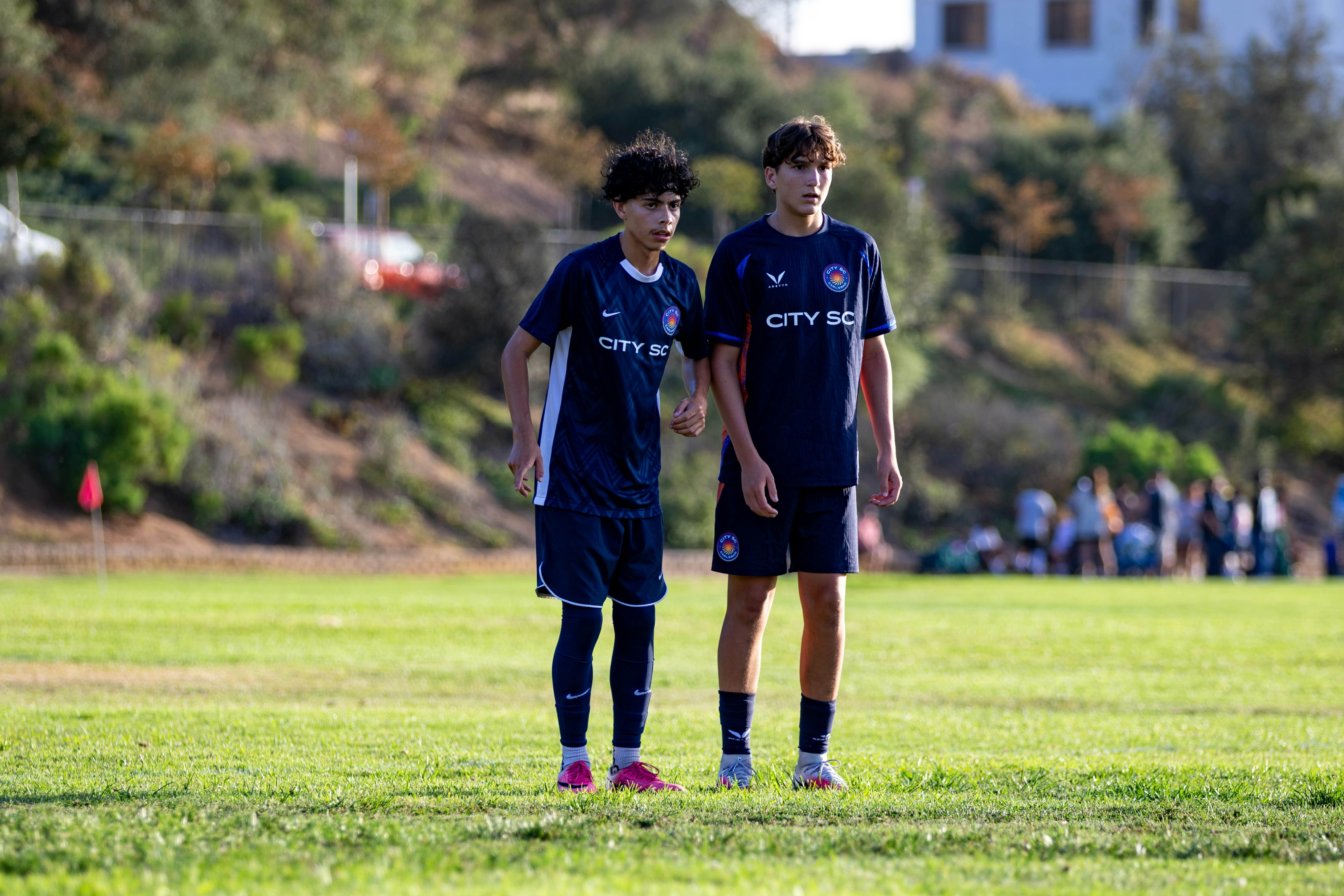 Two teammates pause mid-field, eyes focused toward the game