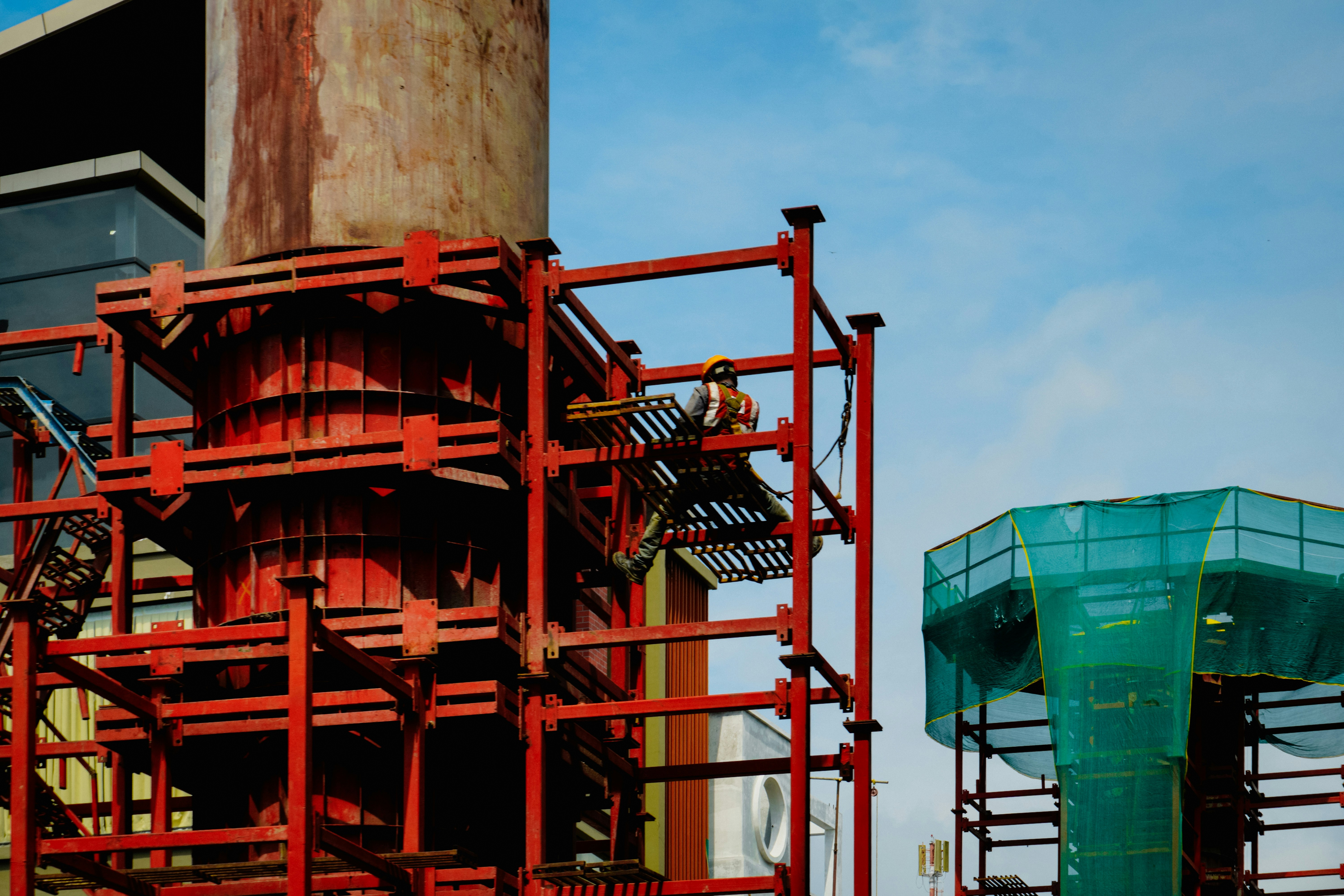 Red Scaffold Symphony: Worker at the Steel Chimney Under a Clear Sky