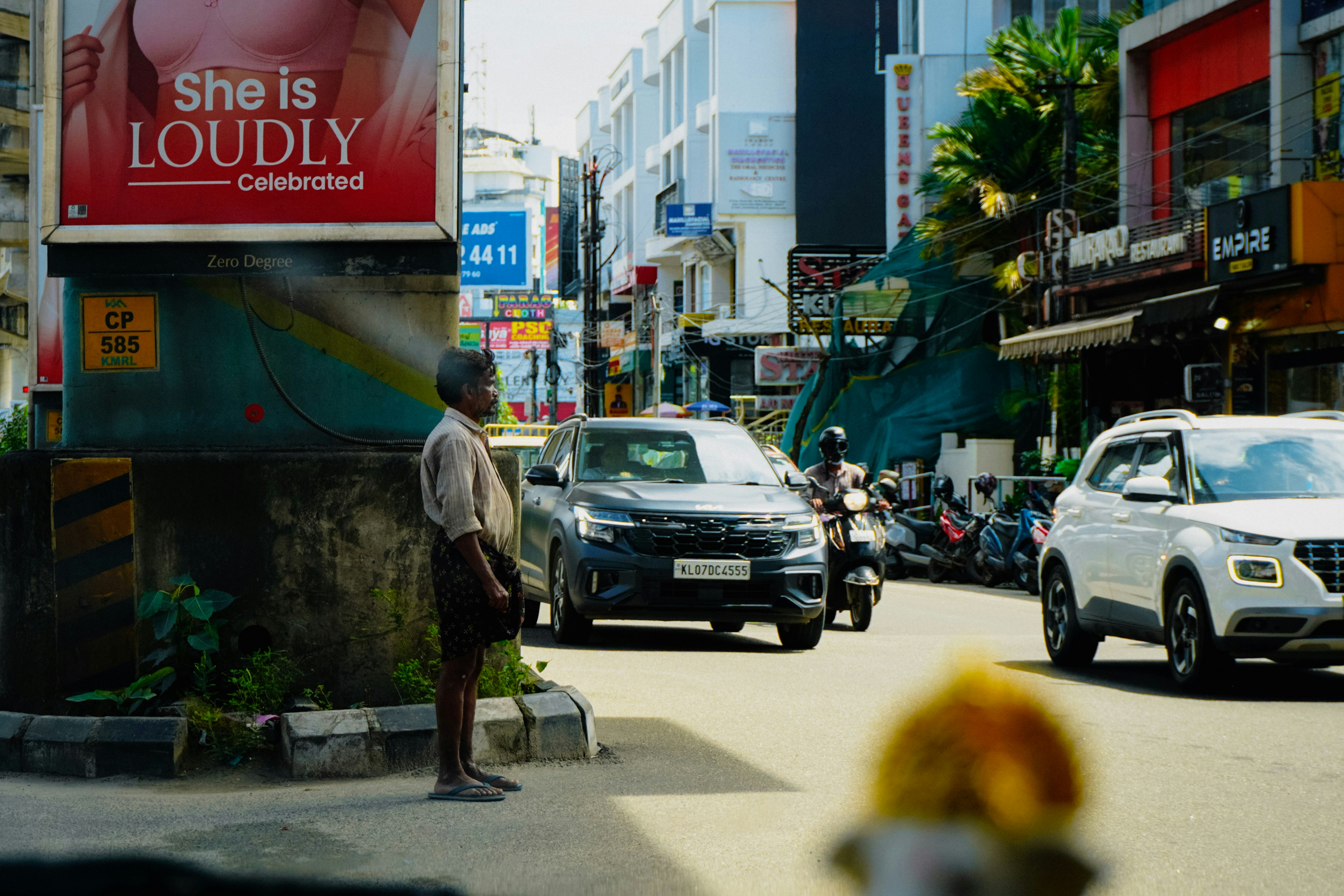 Street Standoff: A Pedestrian Watches Traffic Flow Under Neon-Colored Ads