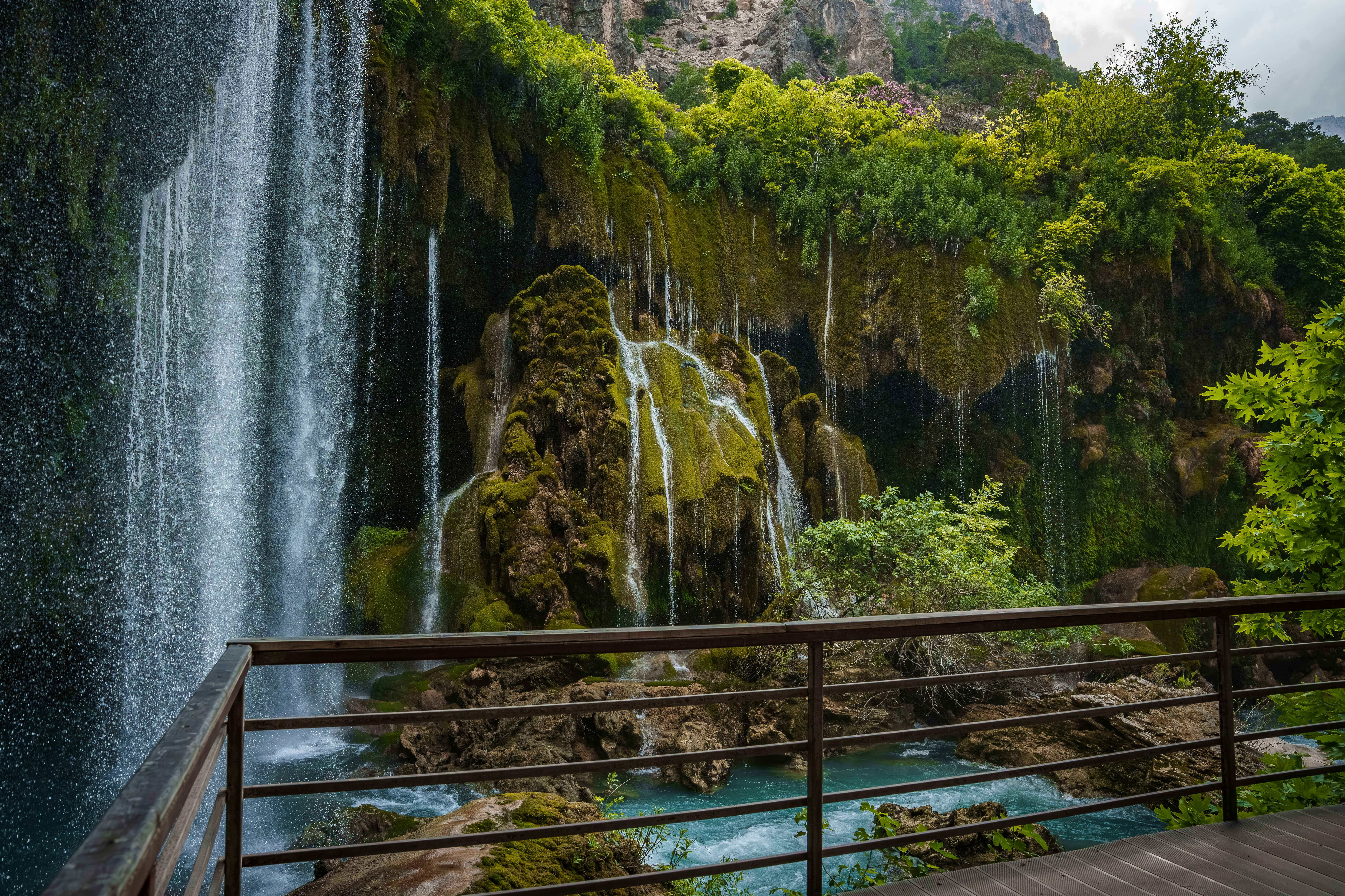 Wooden railing framing a cascading waterfall amid lush canyon walls