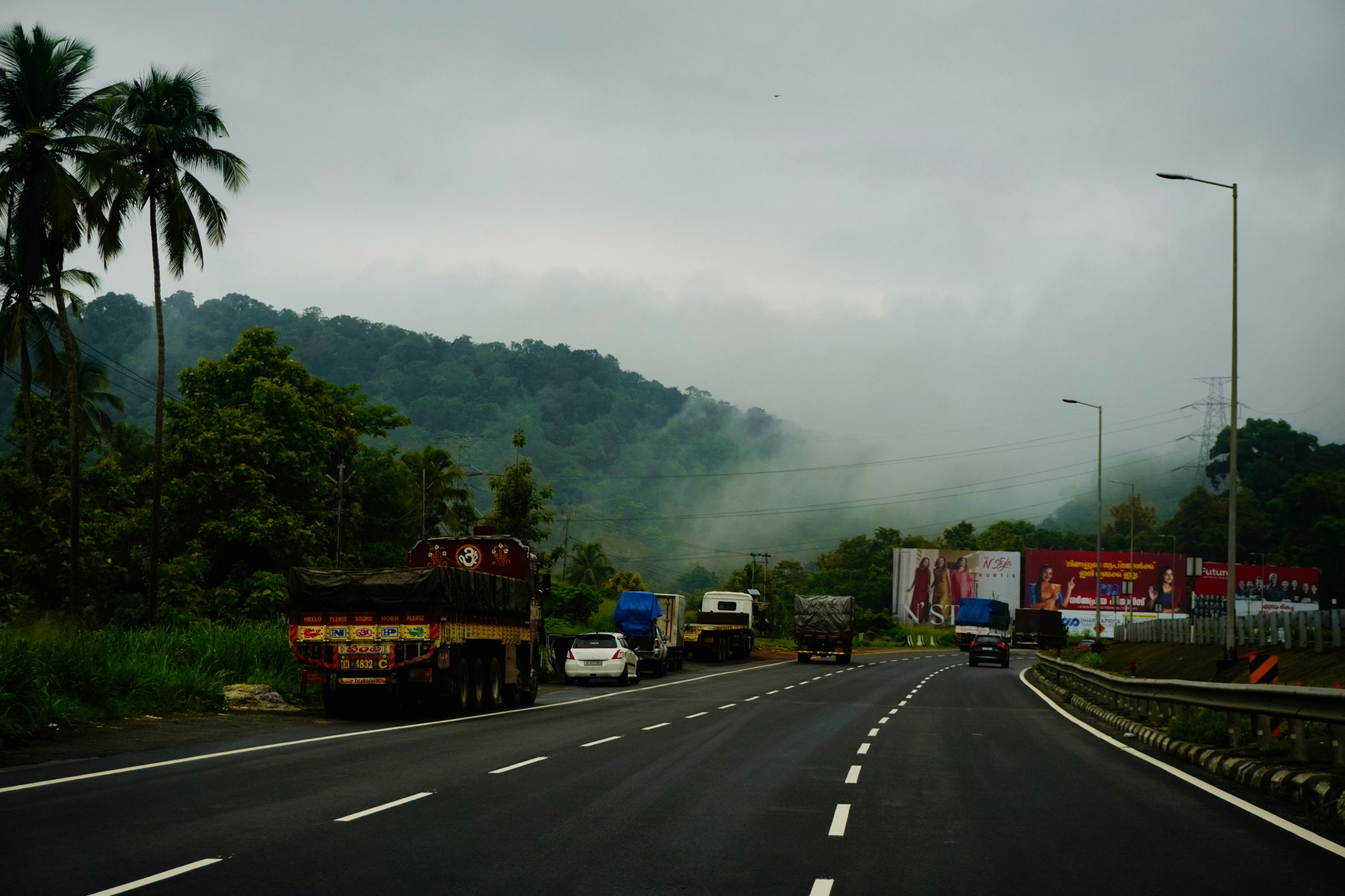 Highway in mist: trucks and palm trees moving toward the distant hills