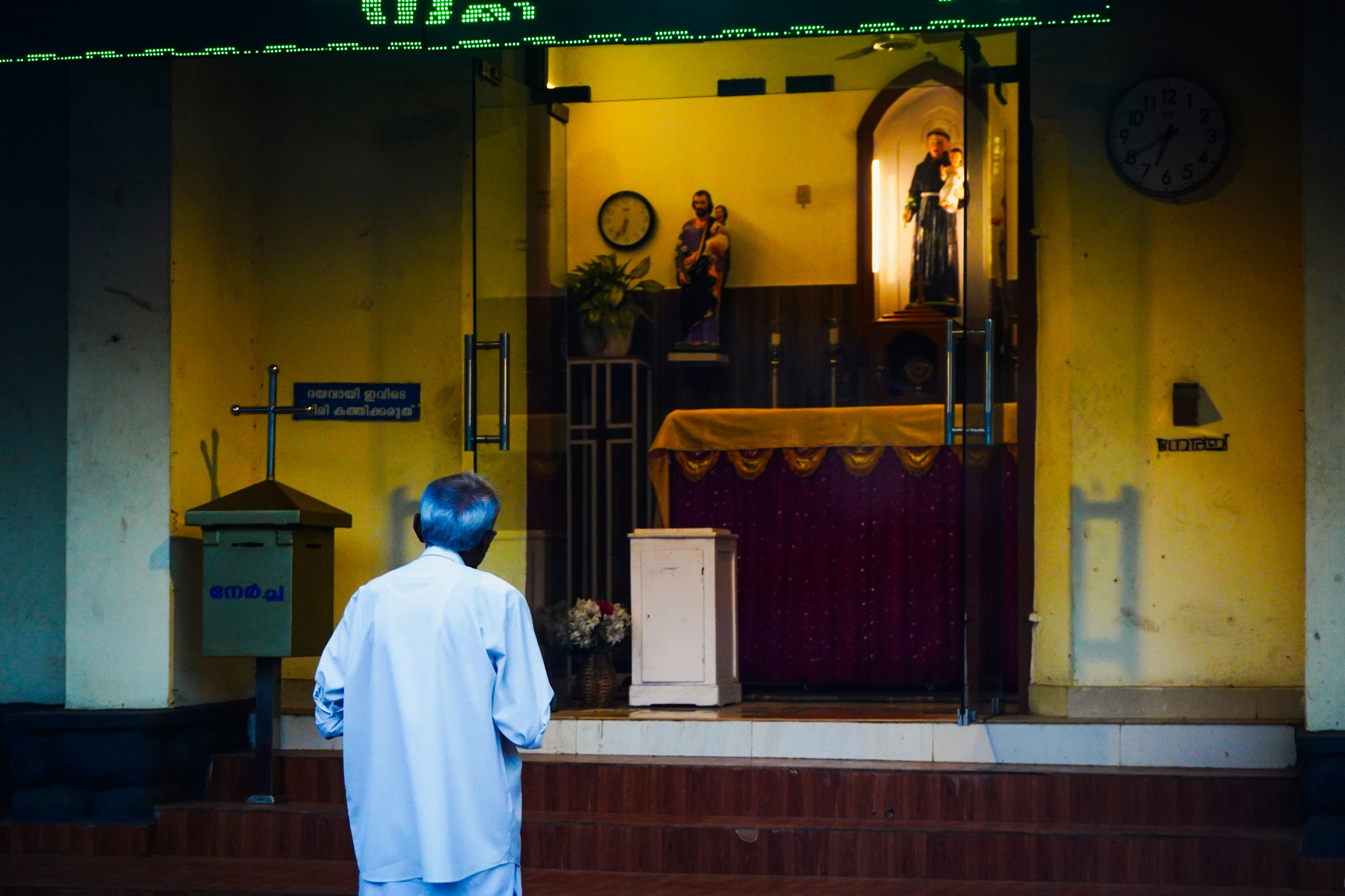 A solitary figure in white faces a religious shrine bathed in warm light