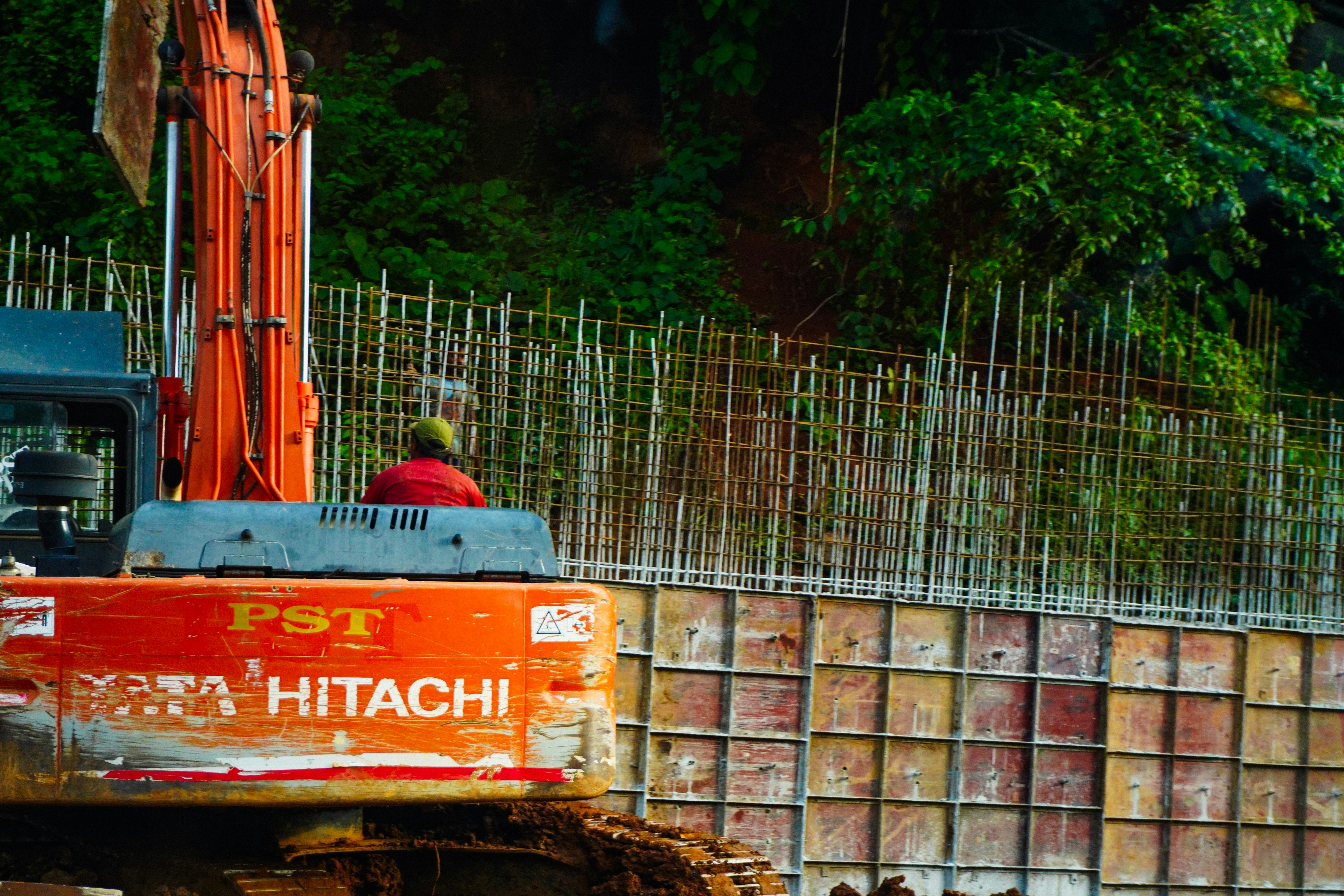Crane at Work: Red Excavator Guarding a Concrete Wall