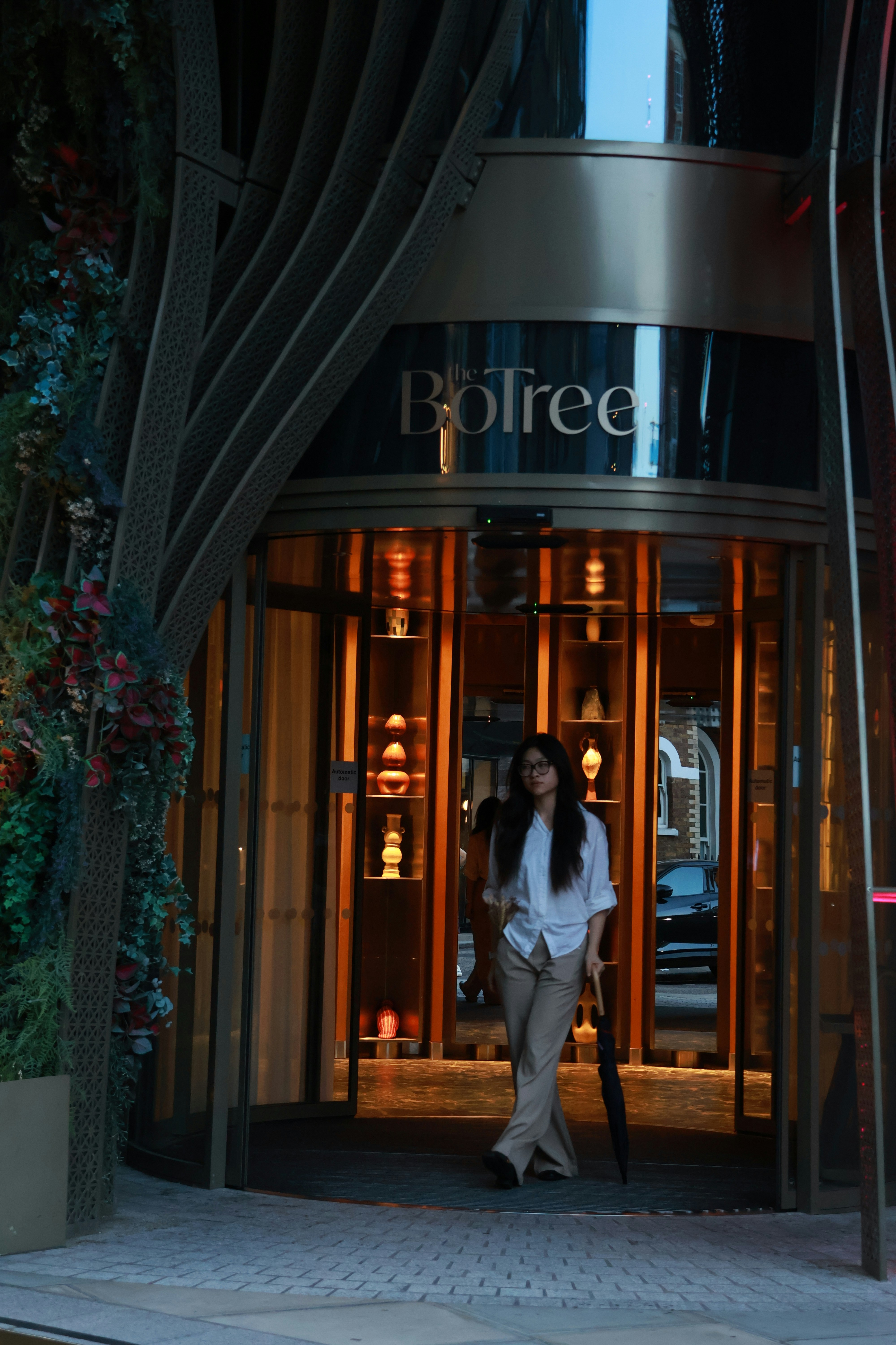 Urban Threshold: Woman Exiting a Boutique Through Glass Doors at Dusk