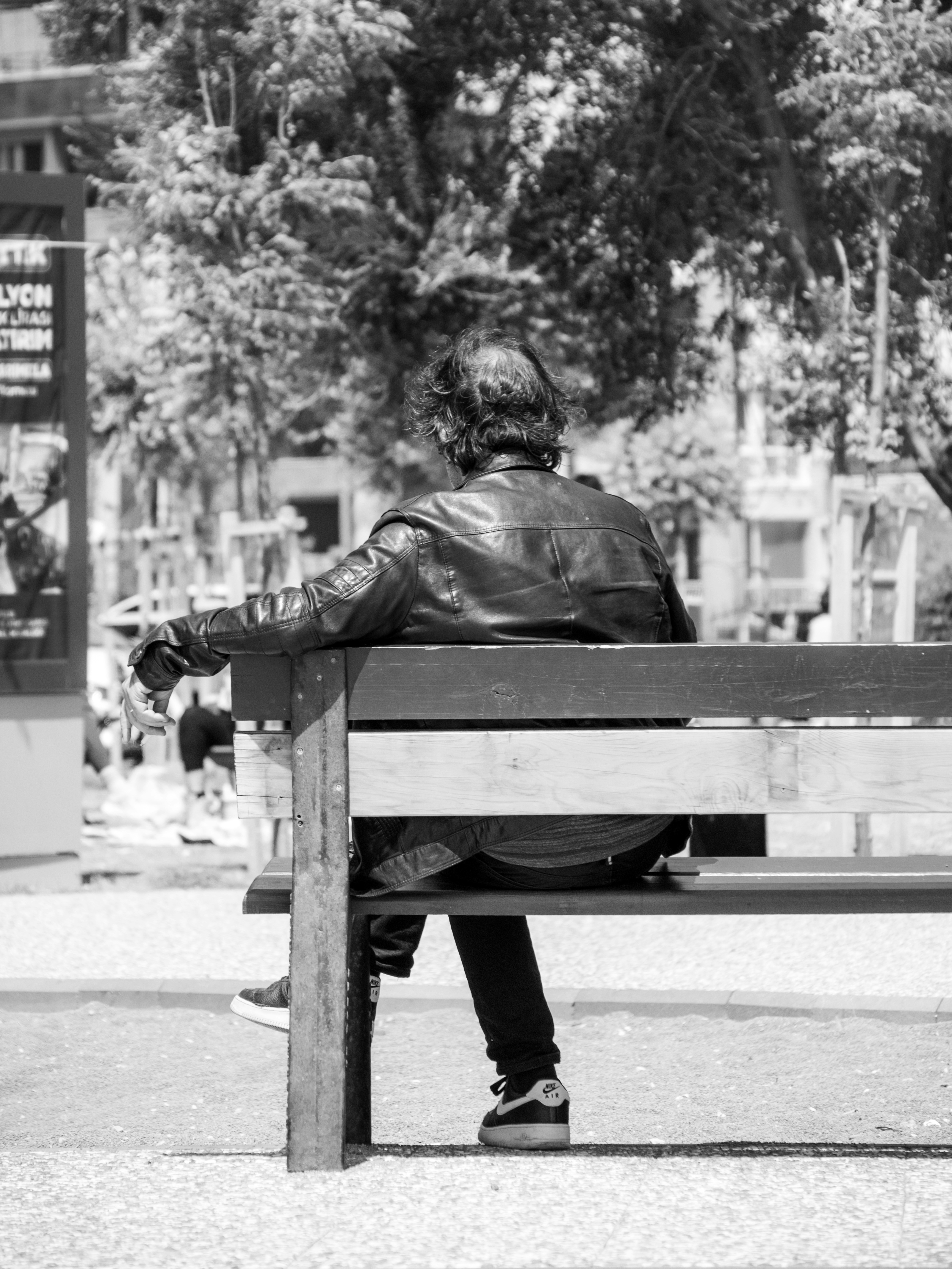 Backlit by the City: A lone figure on a bench in monochrome calm