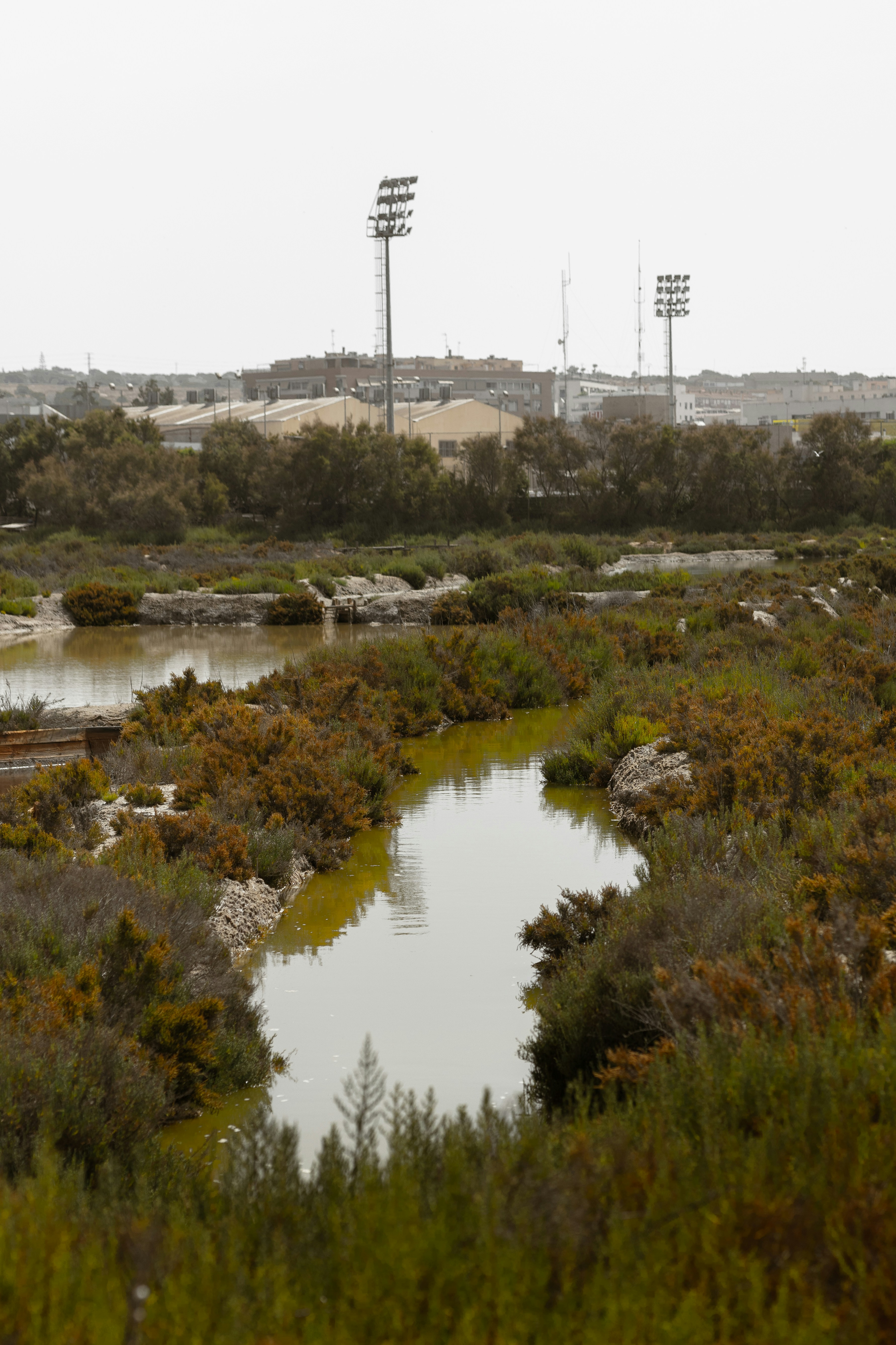 River corridor weaving through coastal scrub toward an industrial backdrop