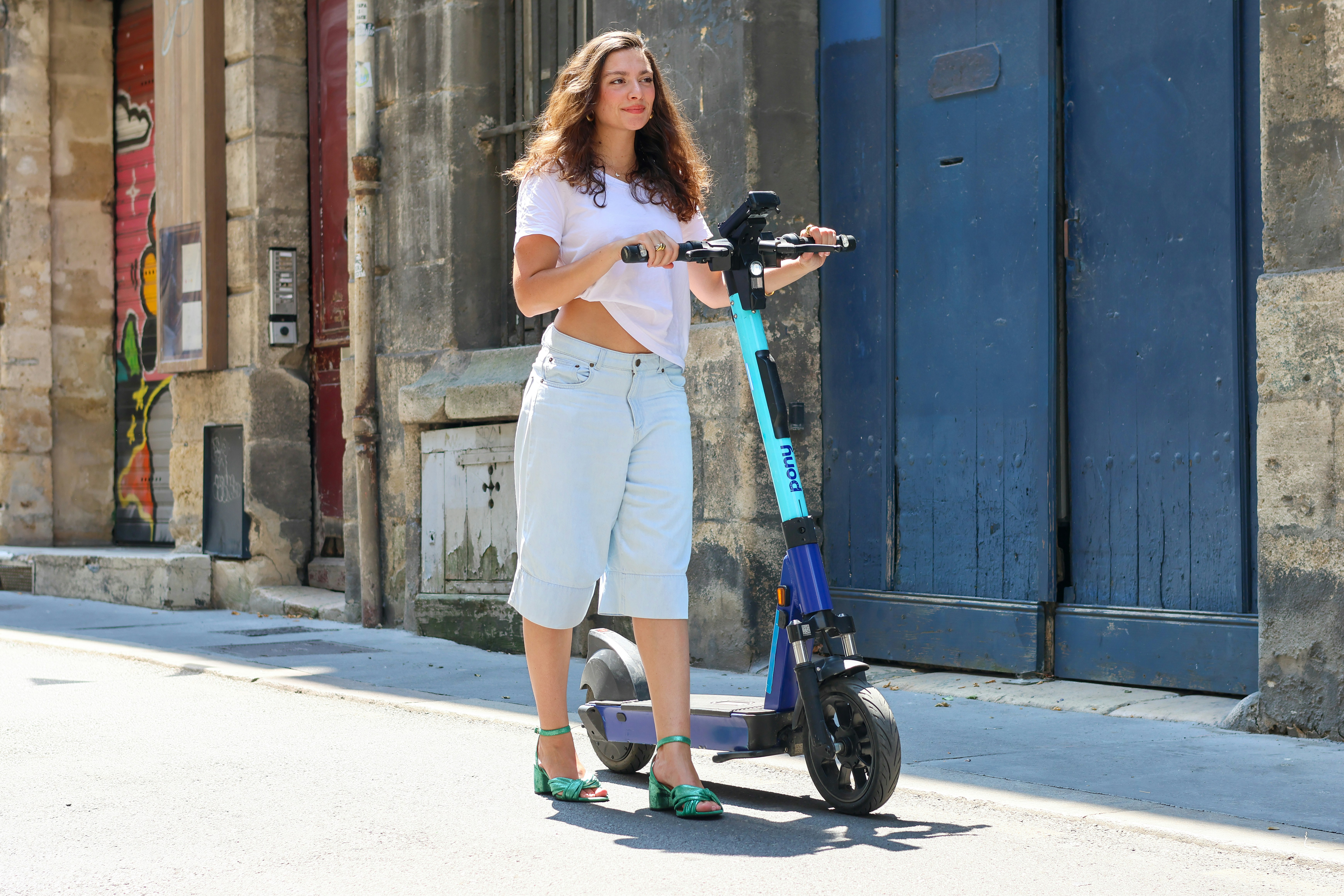 City Street Rider: A young woman with a turquoise scooter pauses by a blue door