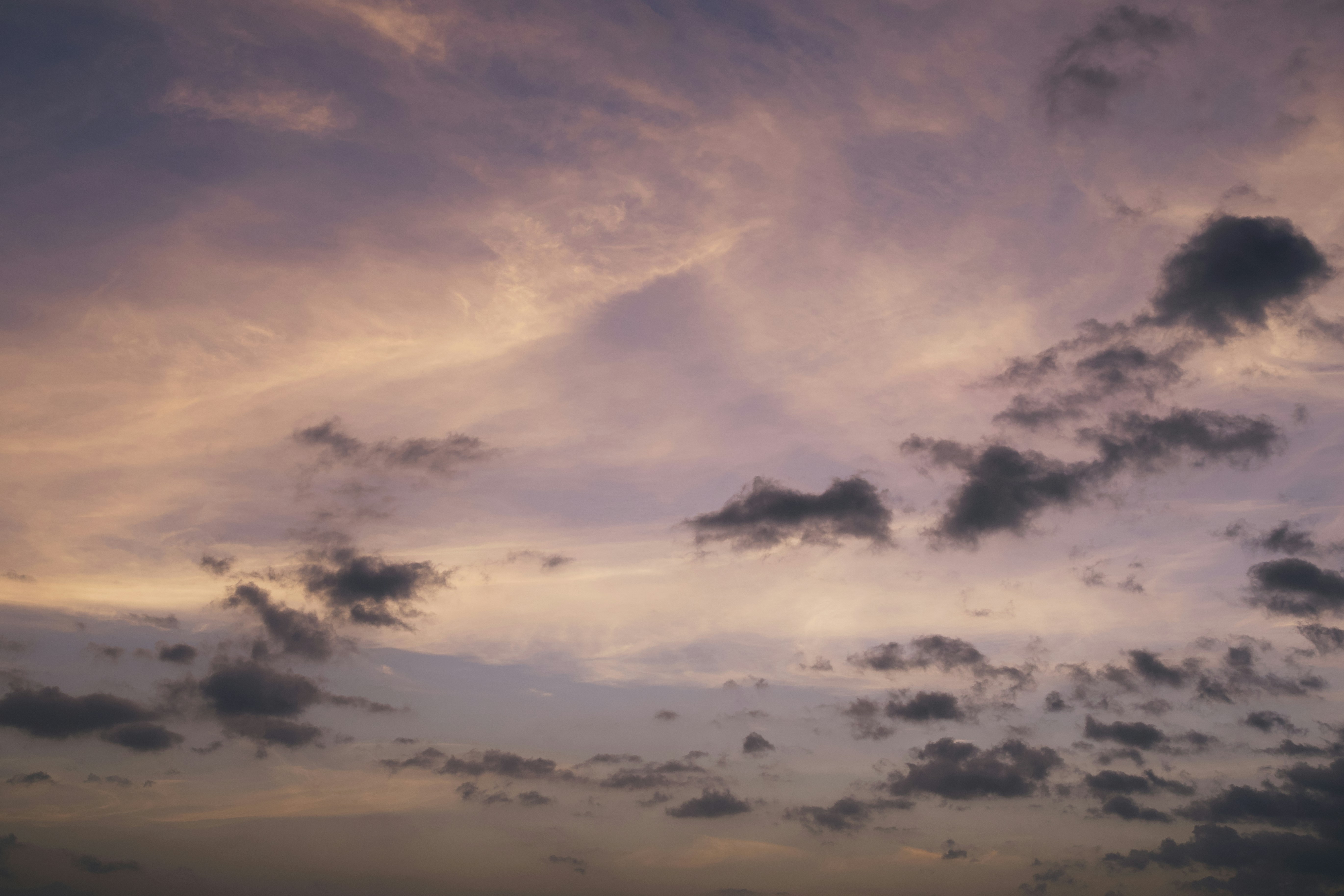 Vibrant pastel clouds drift across a calm horizon at dawn, creating a serene skyscape with warm pinks and cool blues. This is a natural sky photograph.