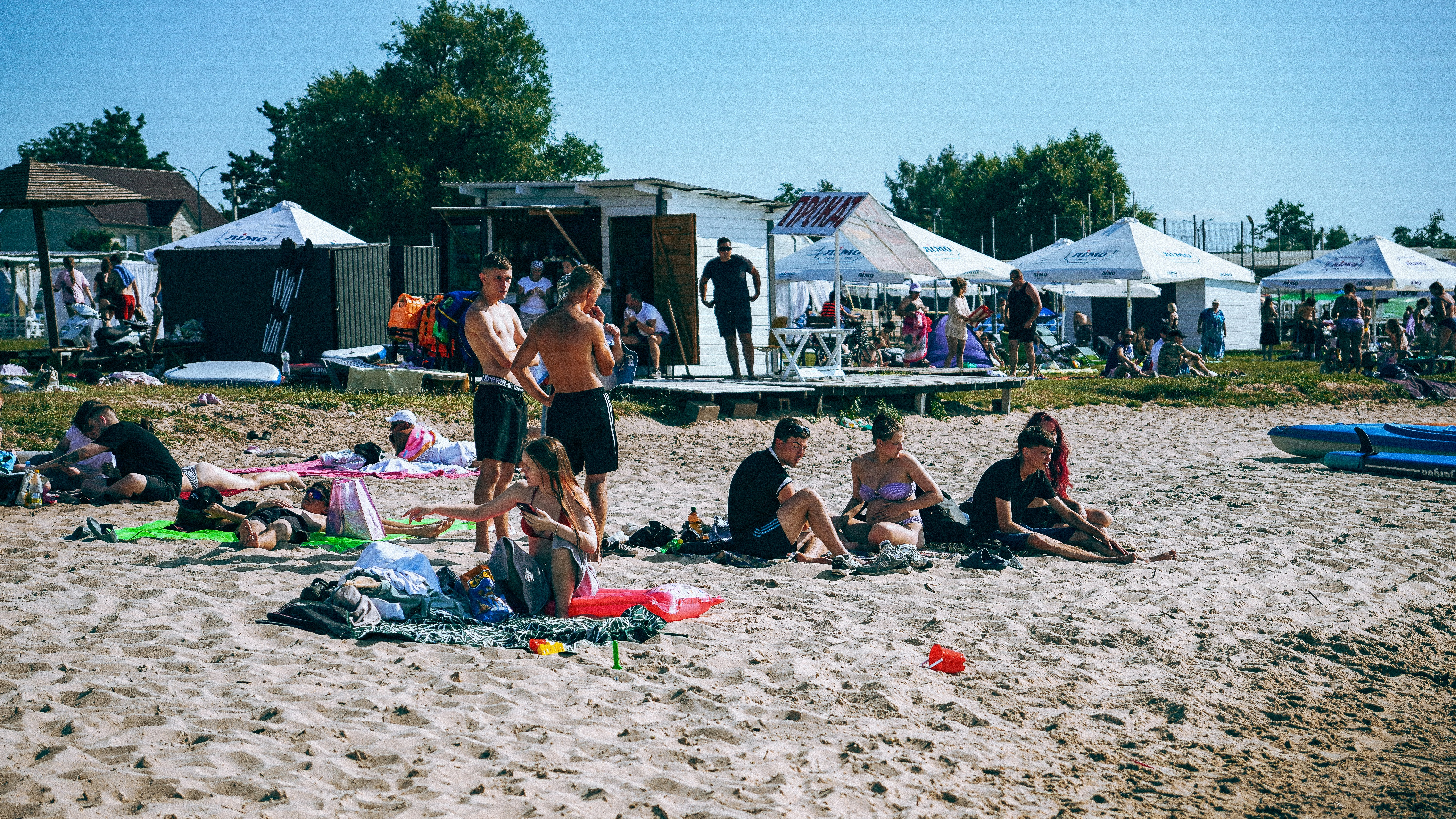 Sunlit Beach Bash: People Gathered Near Tents and Boats on a Busy Shore