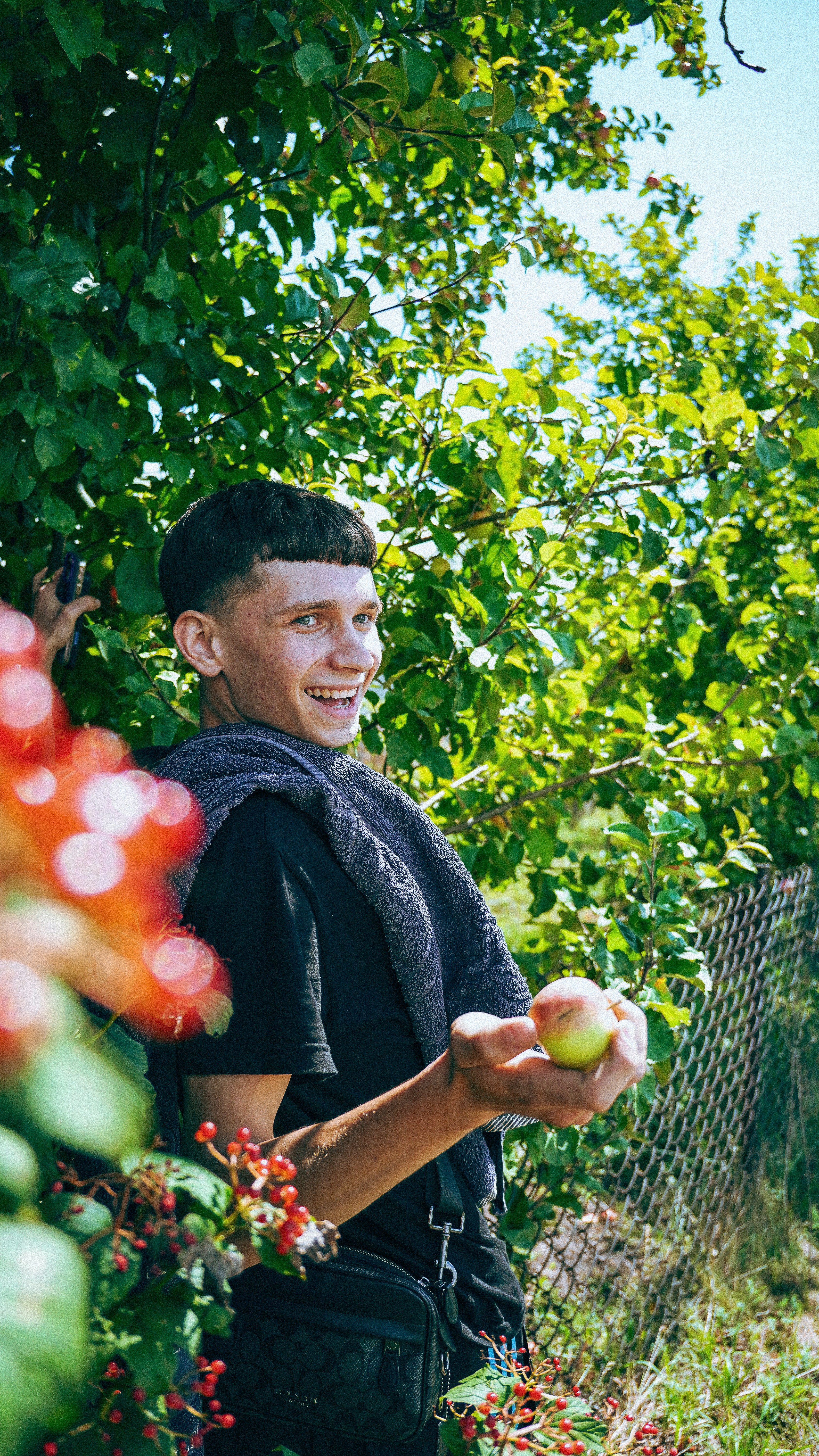 Smiling Gardener in Sunlit Orchard Reaching for an Apple