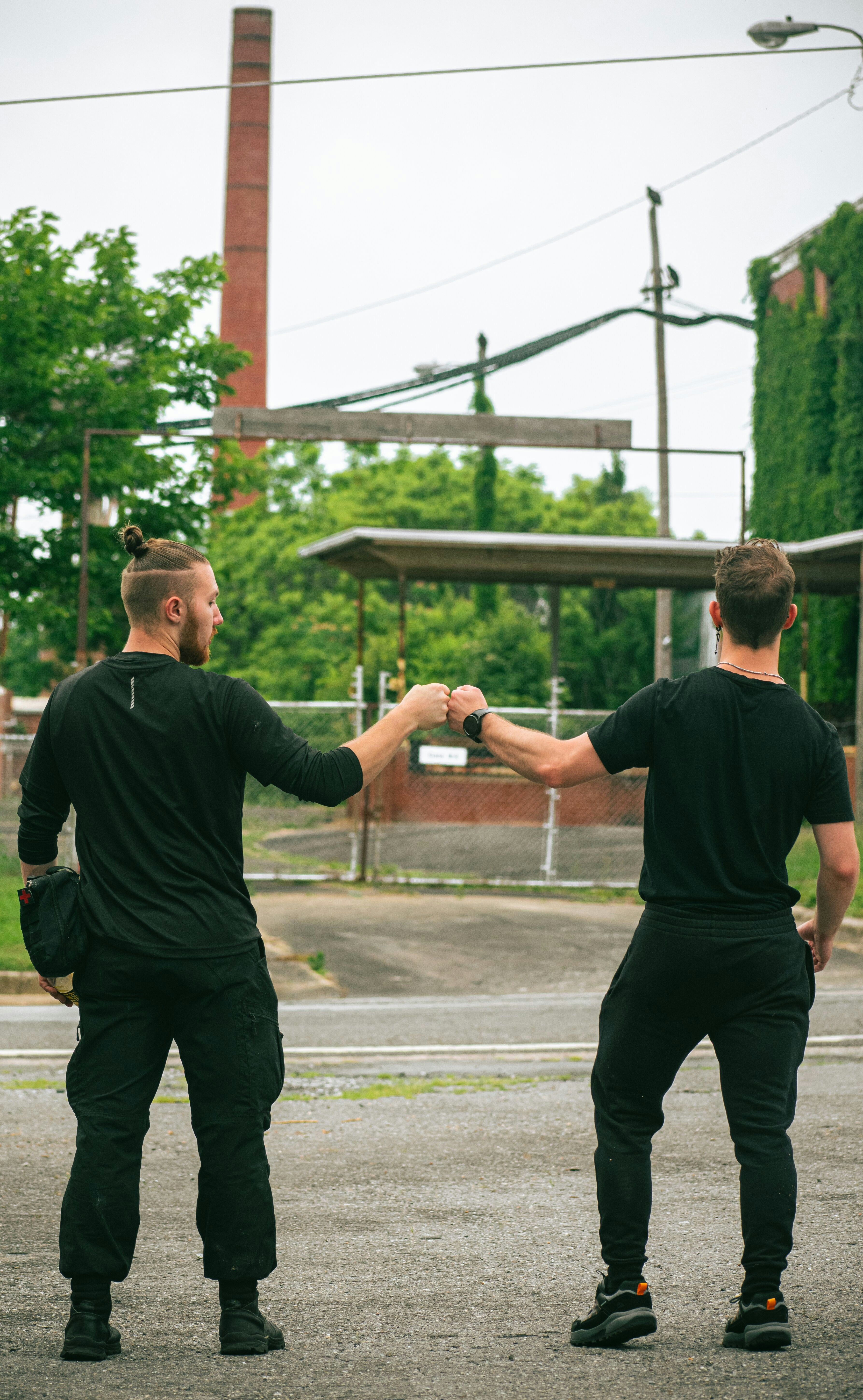 High Five at Dusk: Two Friends in Black on a Quiet Industrial Yard