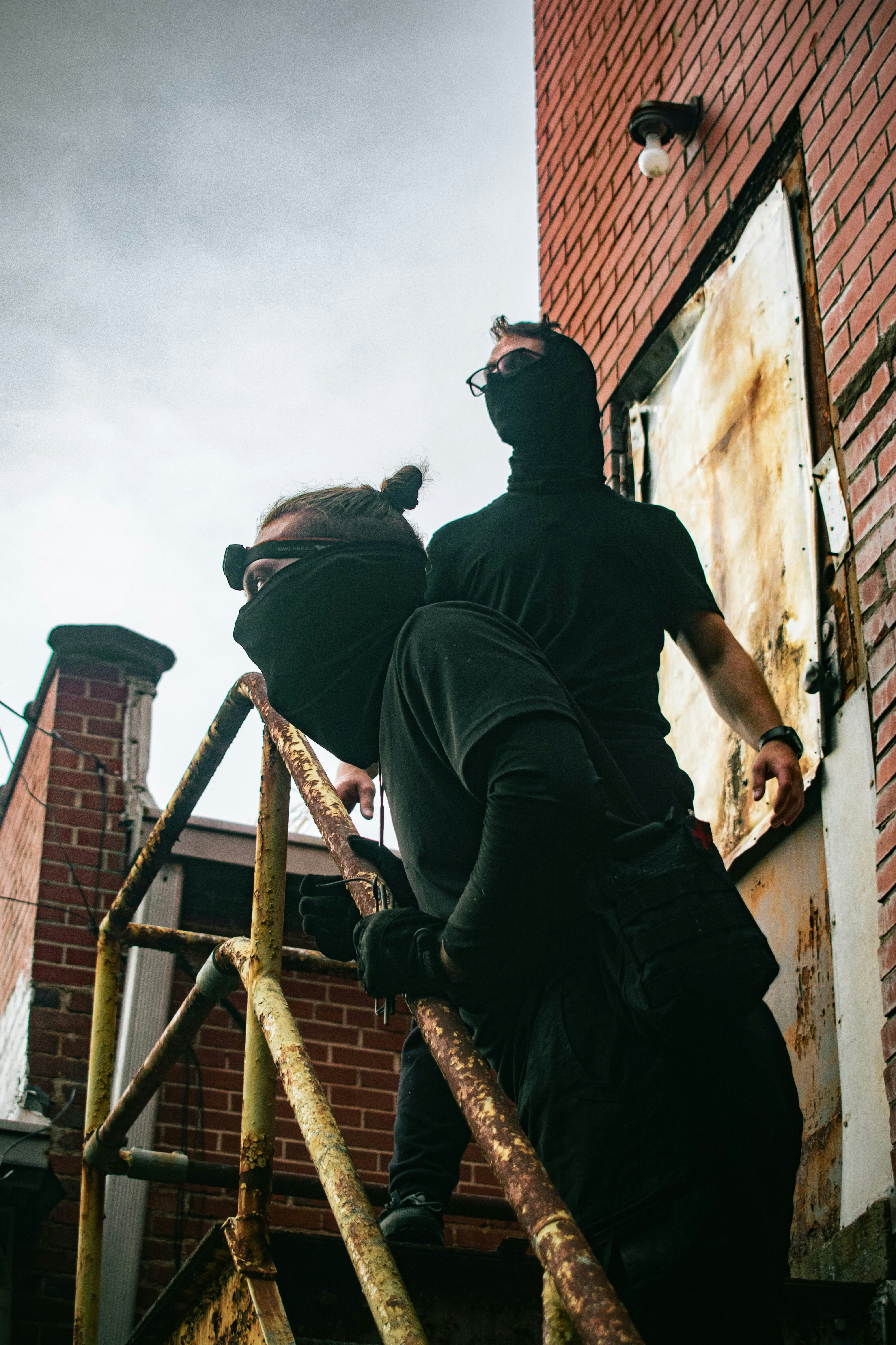 Shadowed Ascent: Two Figures On a Rusted Fire Escape