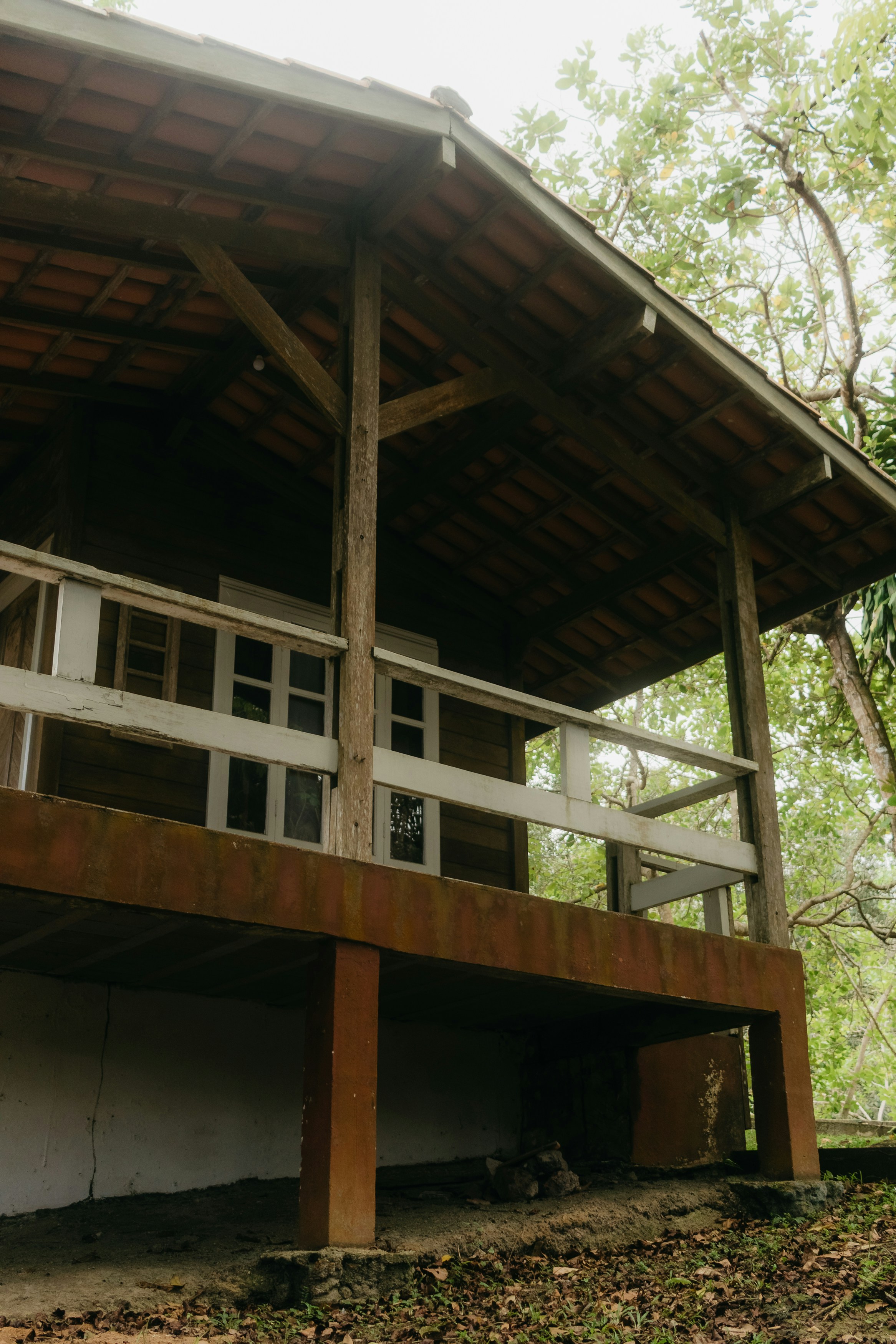 Abandoned wooden porch under a mossy roofline, whose pillars frame a quiet, neglected cabin