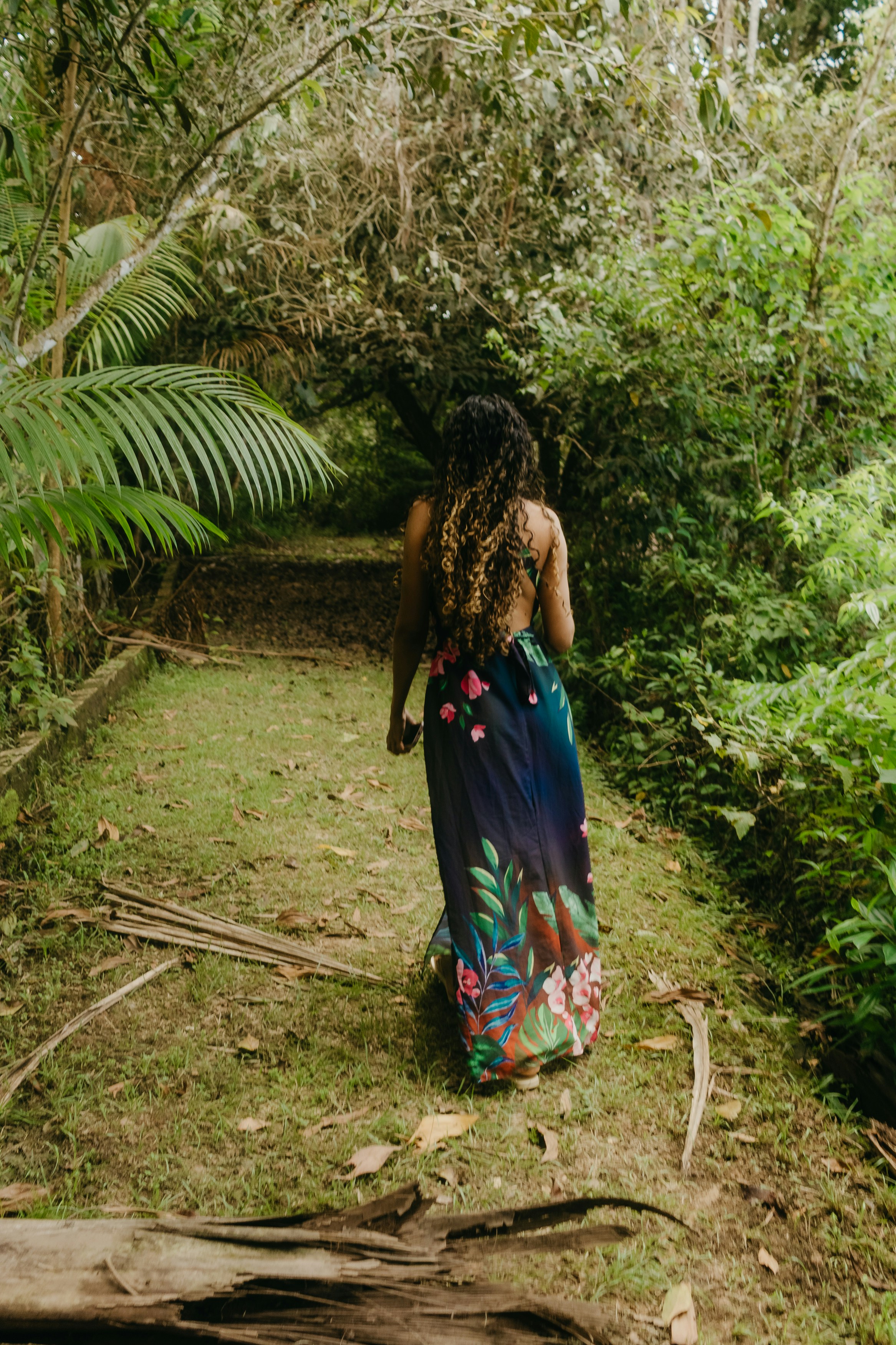 Pathway to Color and Quiet: Woman in a Floral Dress Walks Through a Lush Green Corridor