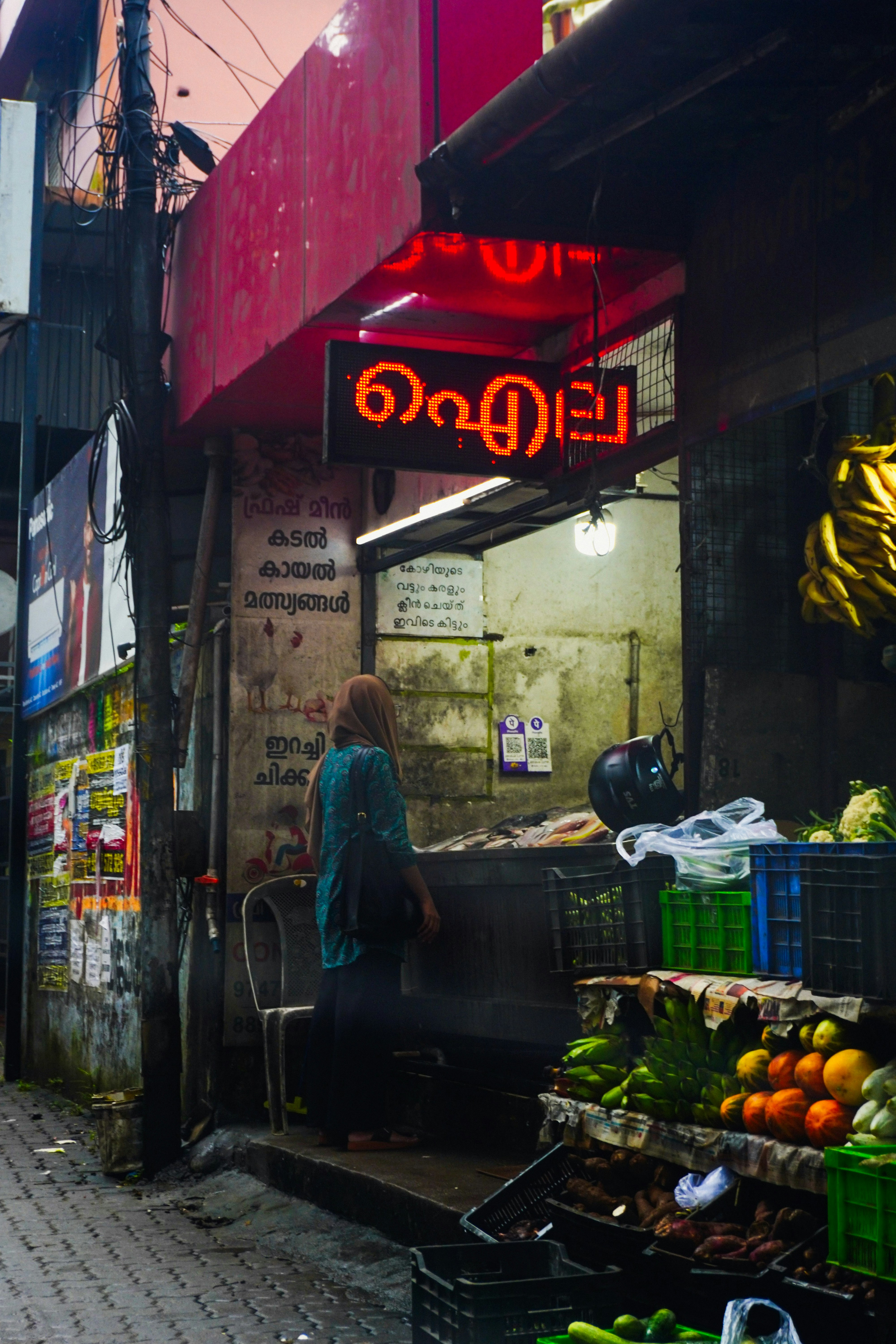 Market Neon and Humble Exchange: A Silhouetted Customer at a Kerala Produce Stall