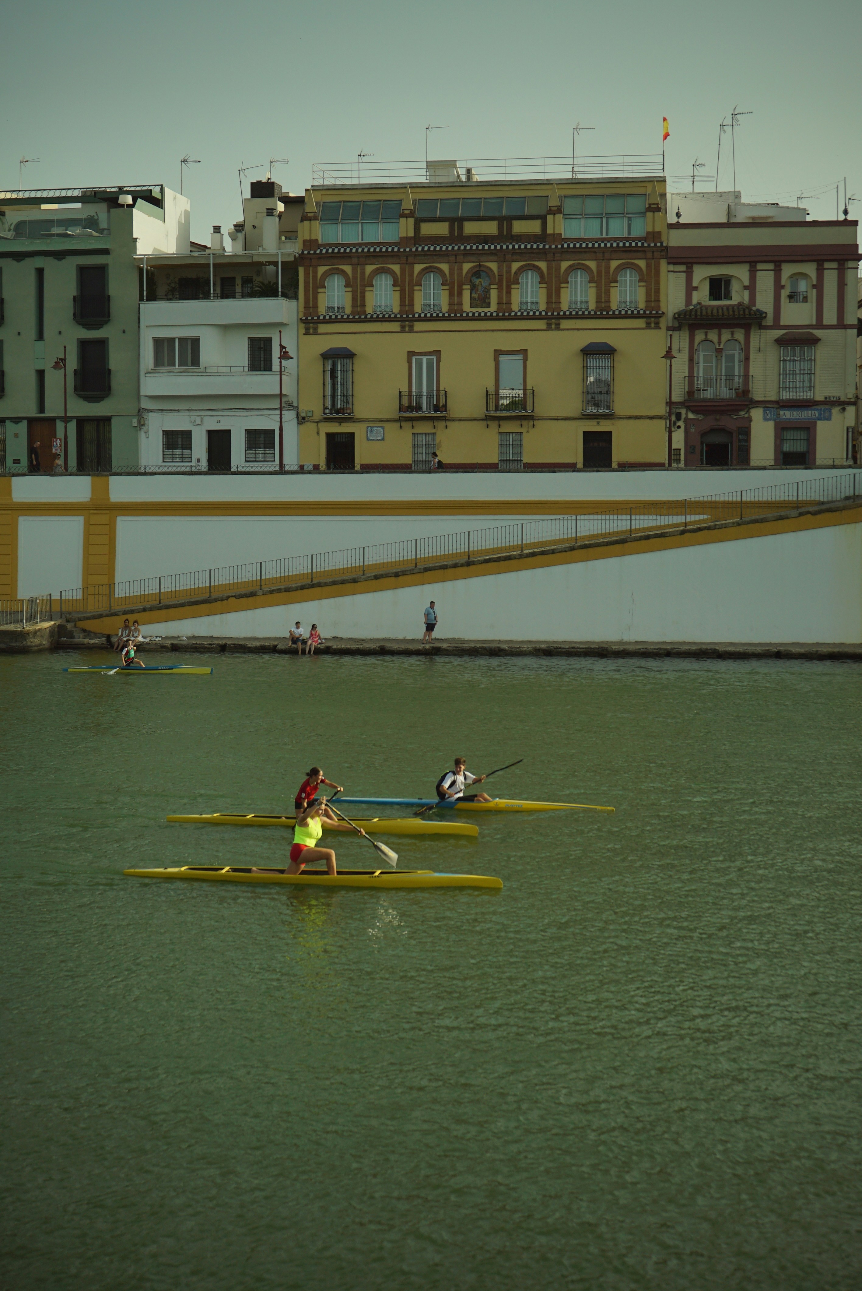 Rowers on a calm canal under a row of pastel buildings