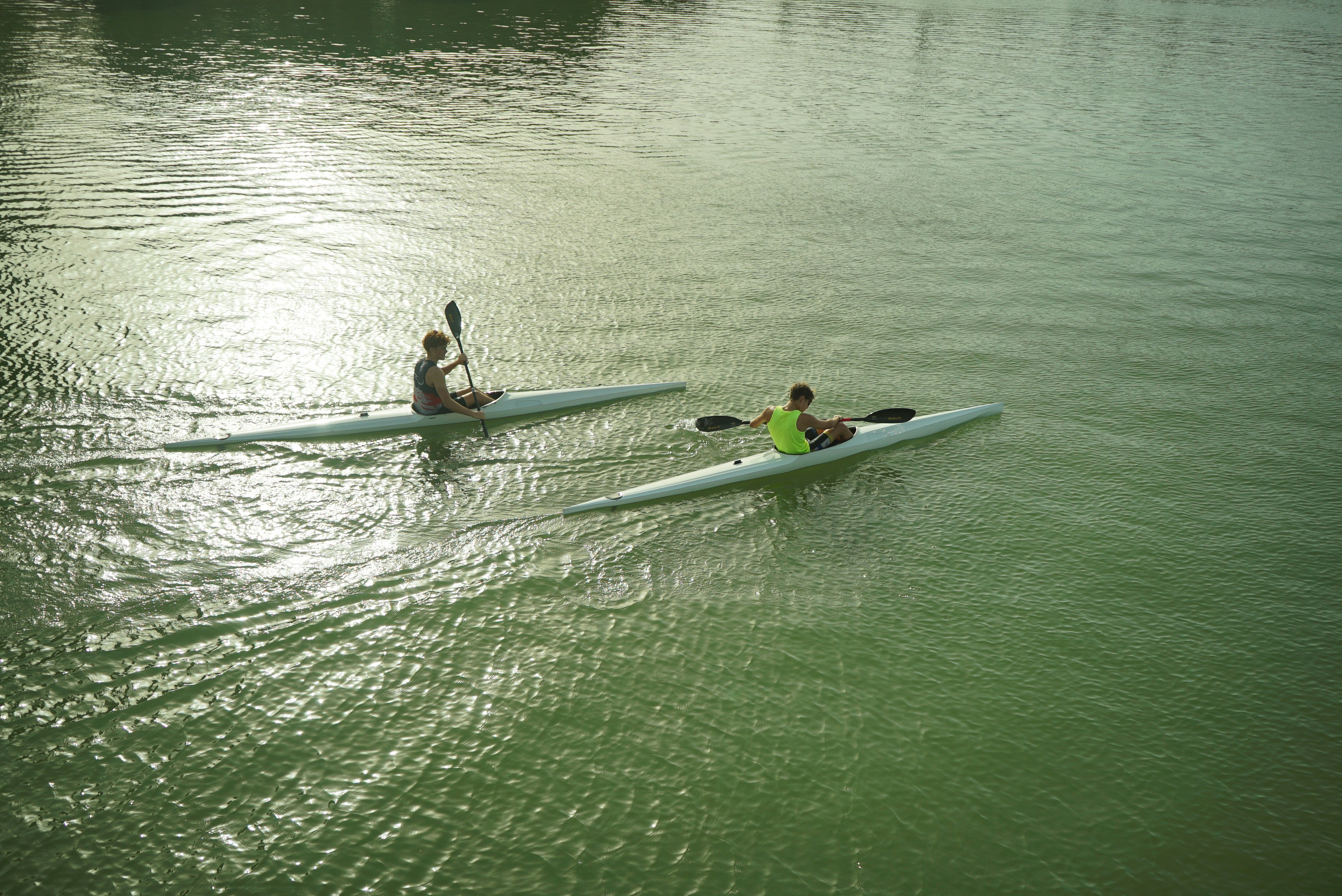 Two Kayaks Cut Through Green Light on a Quiet River
