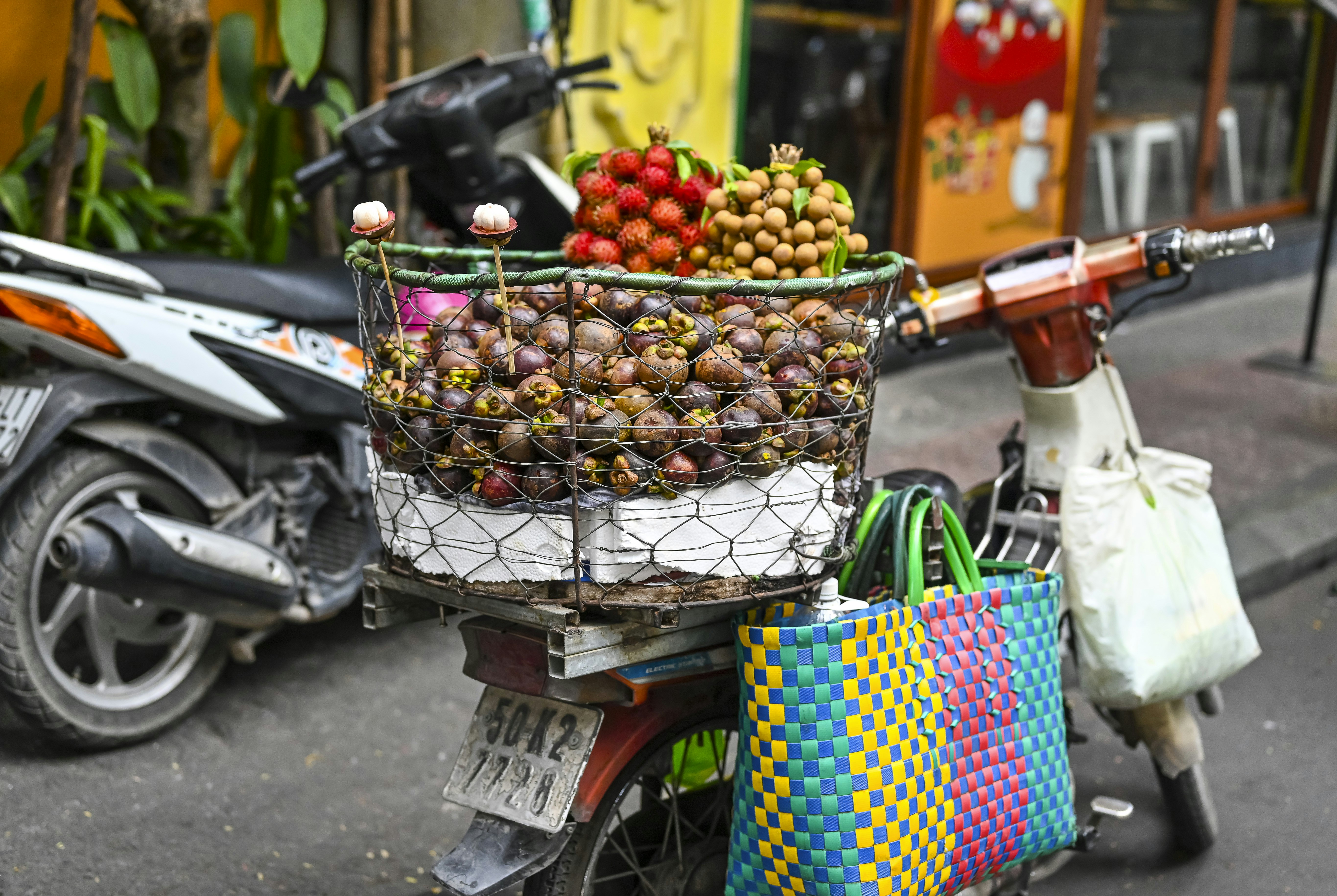 Basket of street fruit on a vintage motorcycle tethered to a busy alleyway