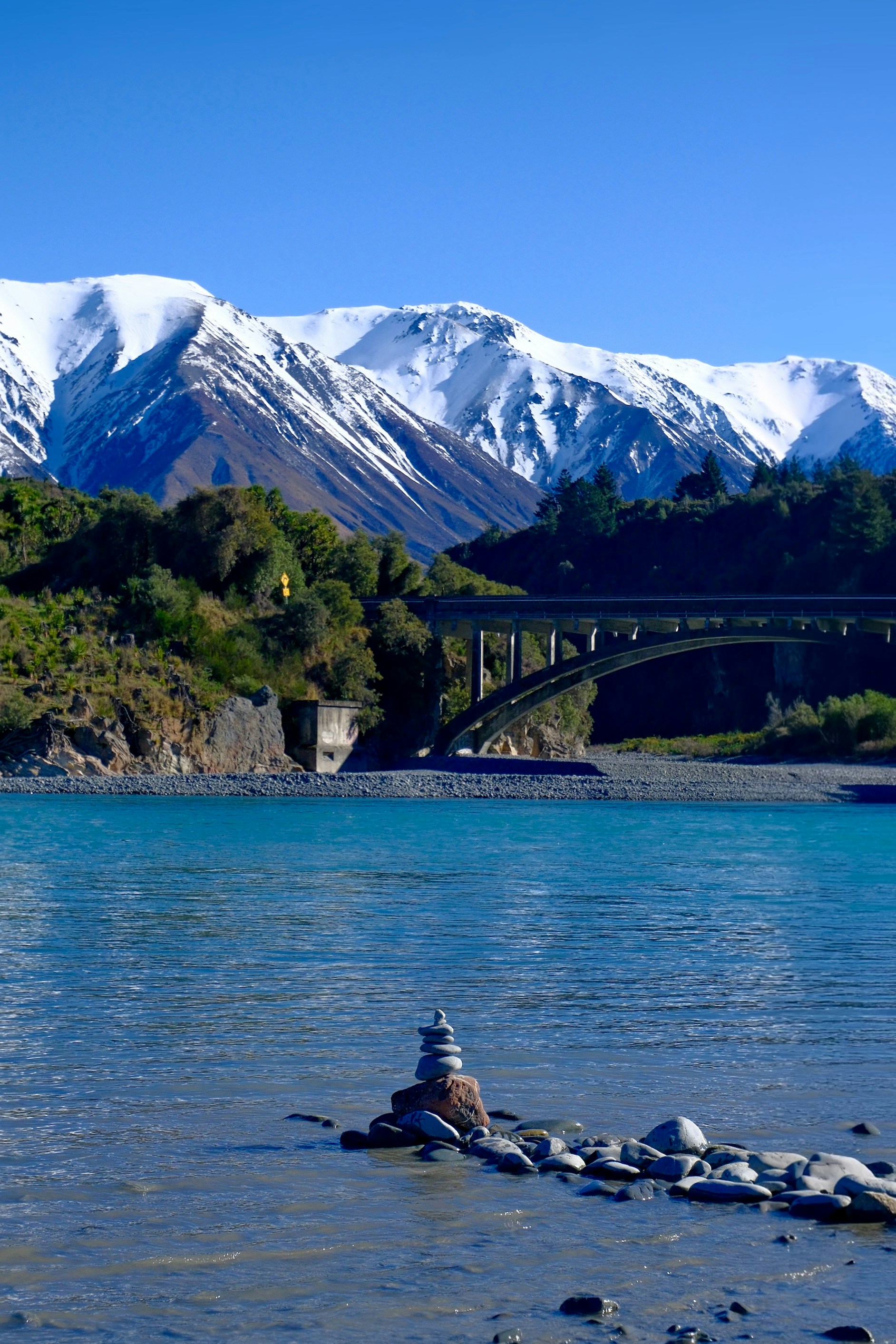 Snow-capped Peaks Over a Serene River with a Stone Stack in the Foreground