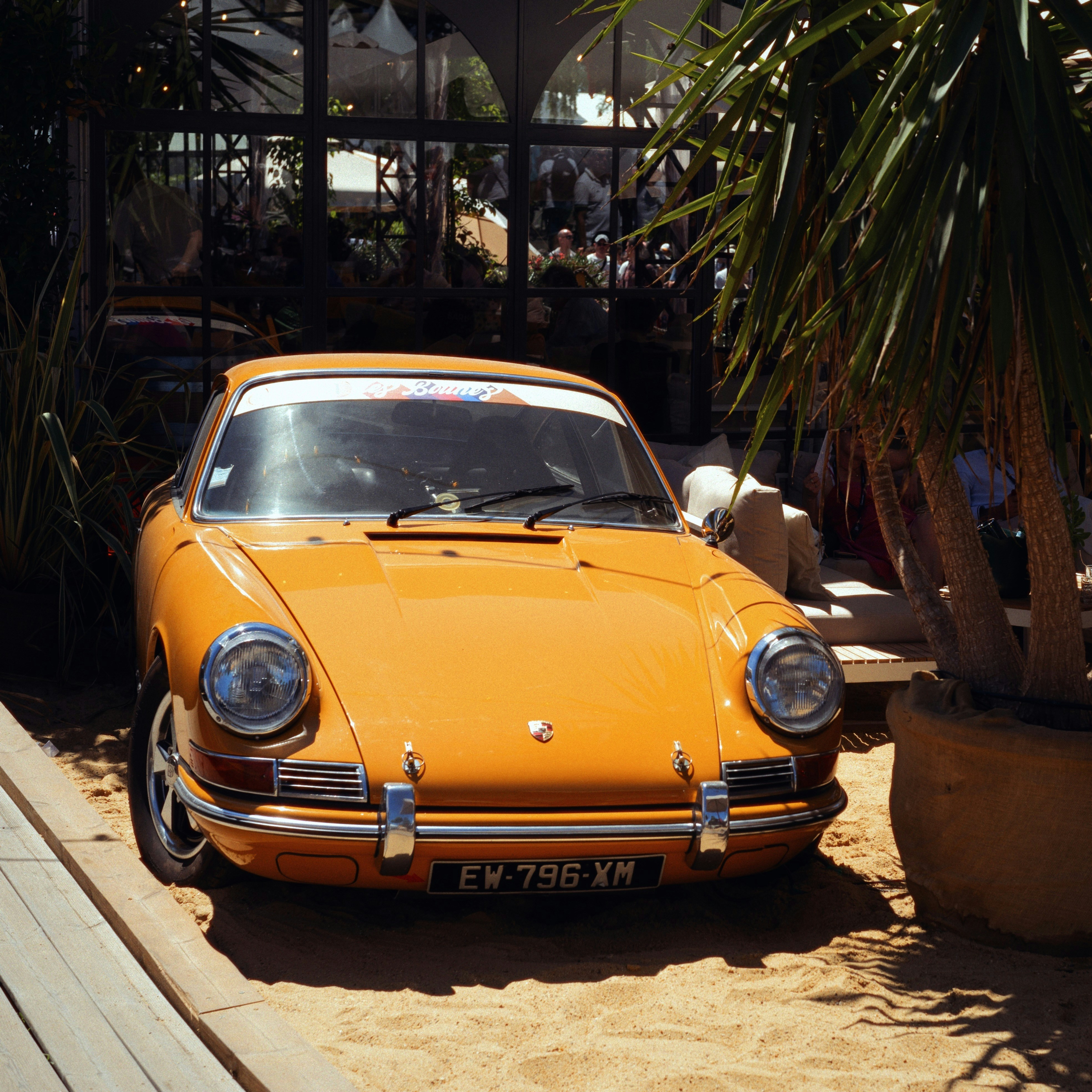 An orange vintage car parked outdoors next to a plant.