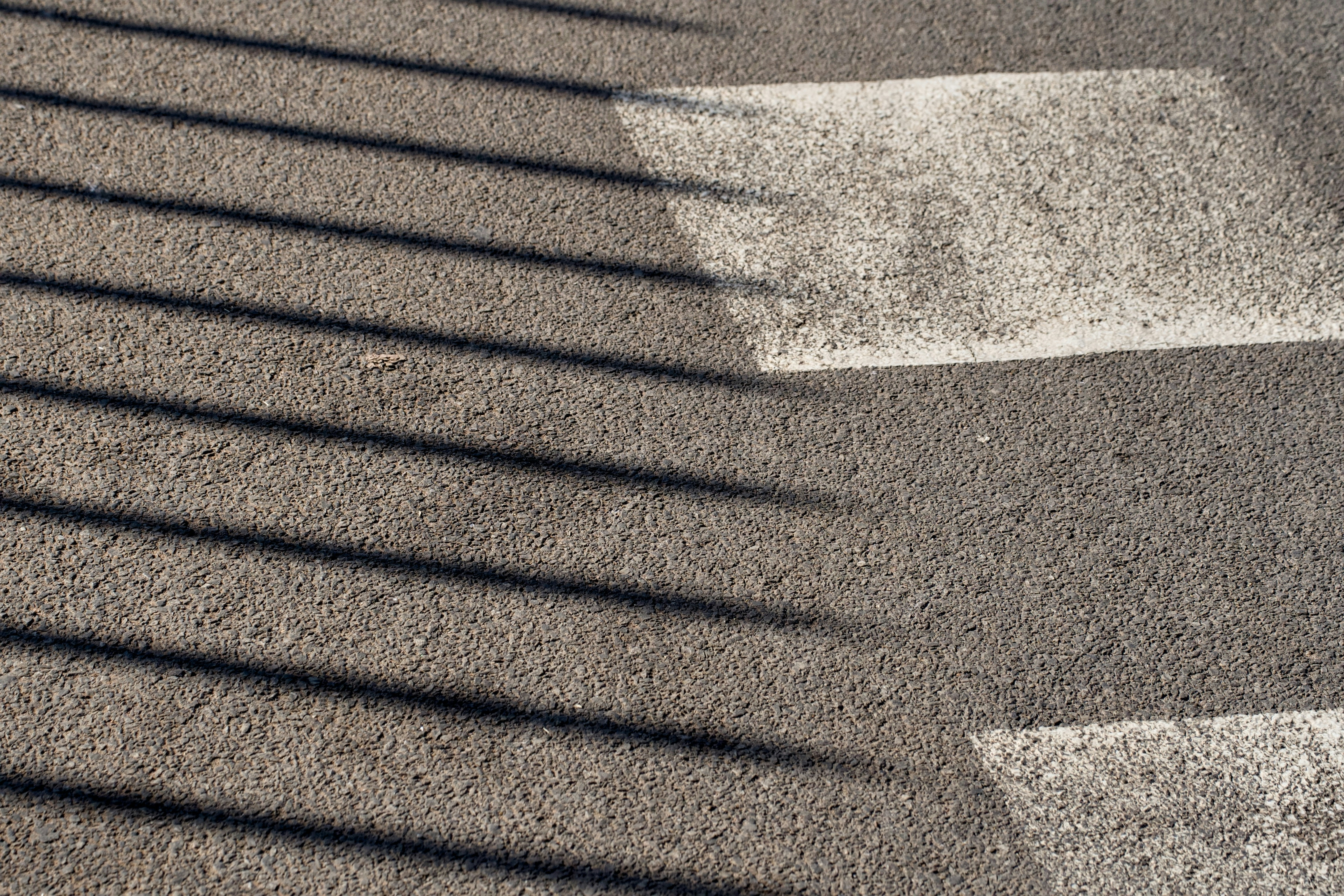 Crosswalk markings and asphalt texture create repeating diagonal shadows and geometric shapes essential to street photography composition.