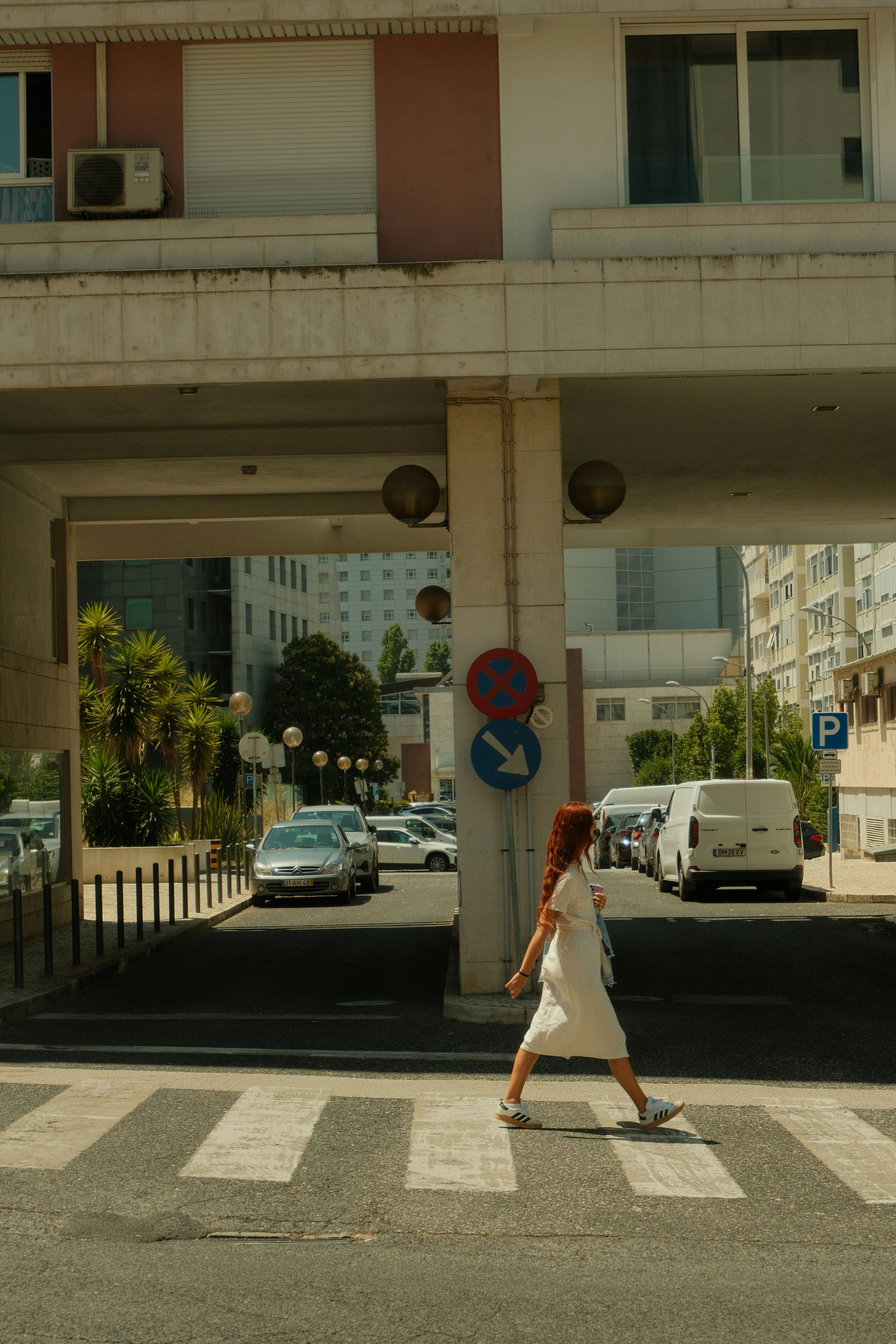 Crosswalk Moment: Woman in White Stride Under Urban Canopy