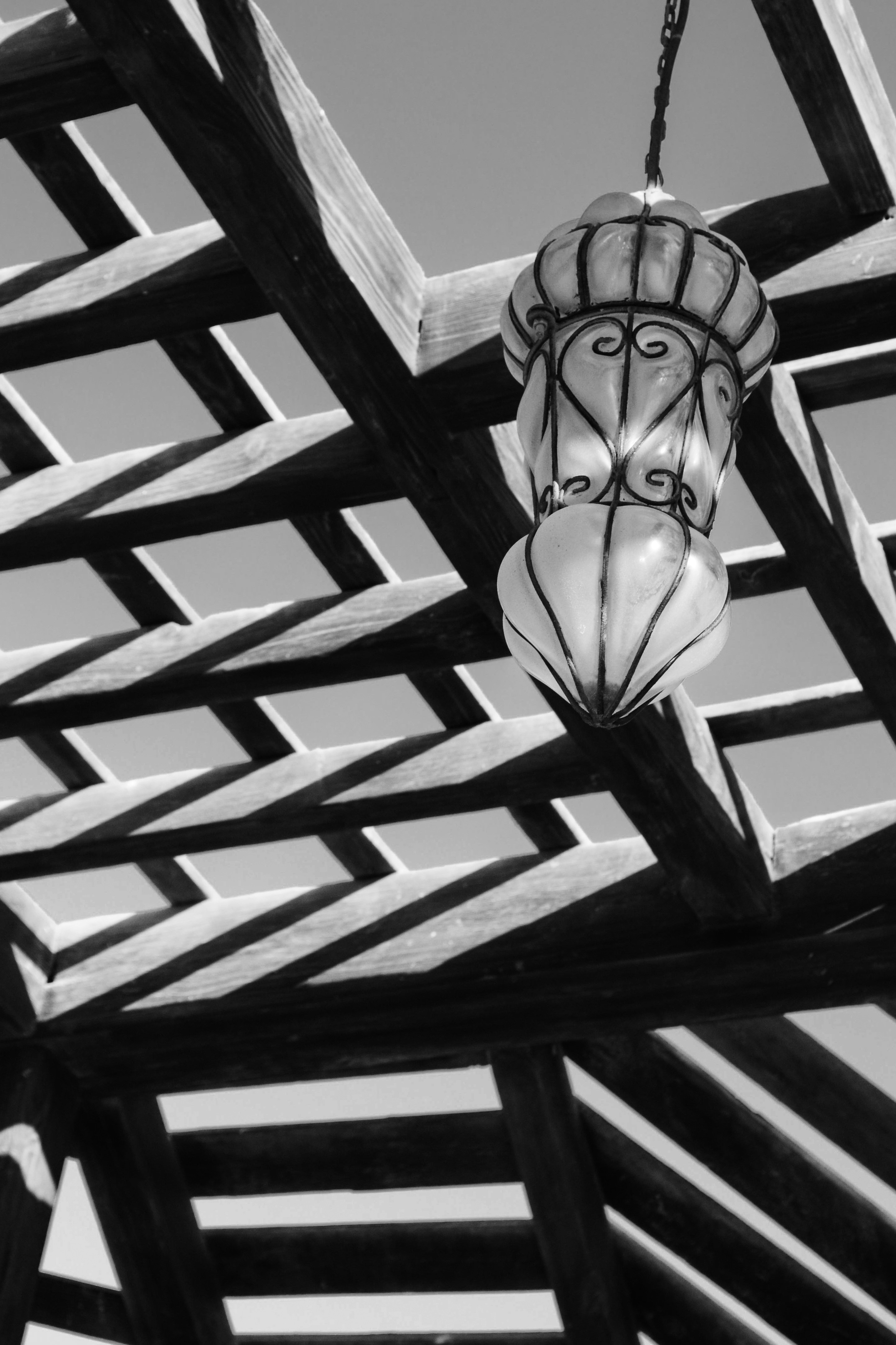 A hanging lantern sits against an intricate wooden lattice in black and white, emphasizing contrast and geometric repetition of lines and shadows.