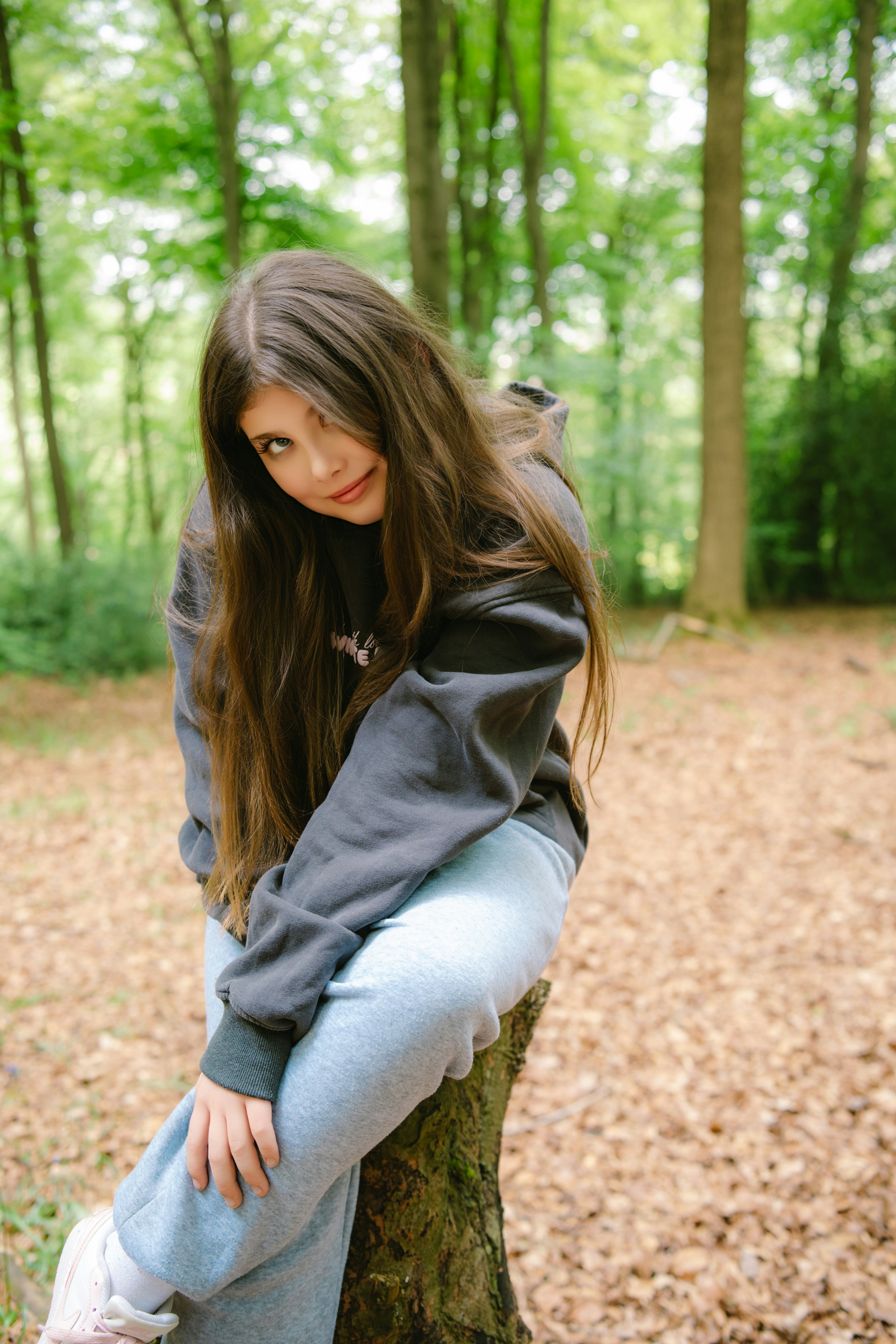 Girl in a Hoodie Perches on a Forest Trunk, Soft Light Filtering Through Pines