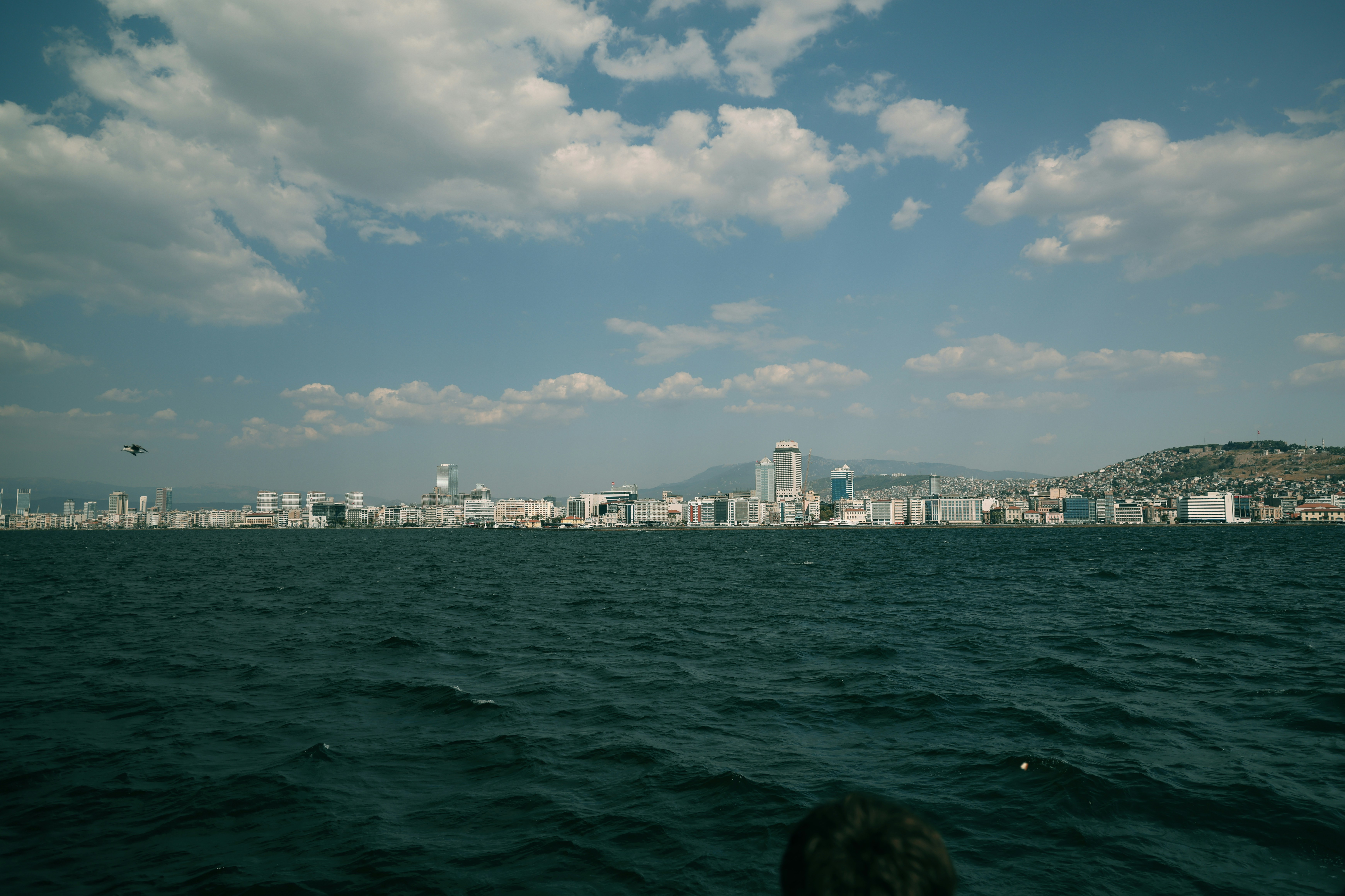 Vast sea foreground with a distant skyline along the coast and a bright, partly cloudy sky.