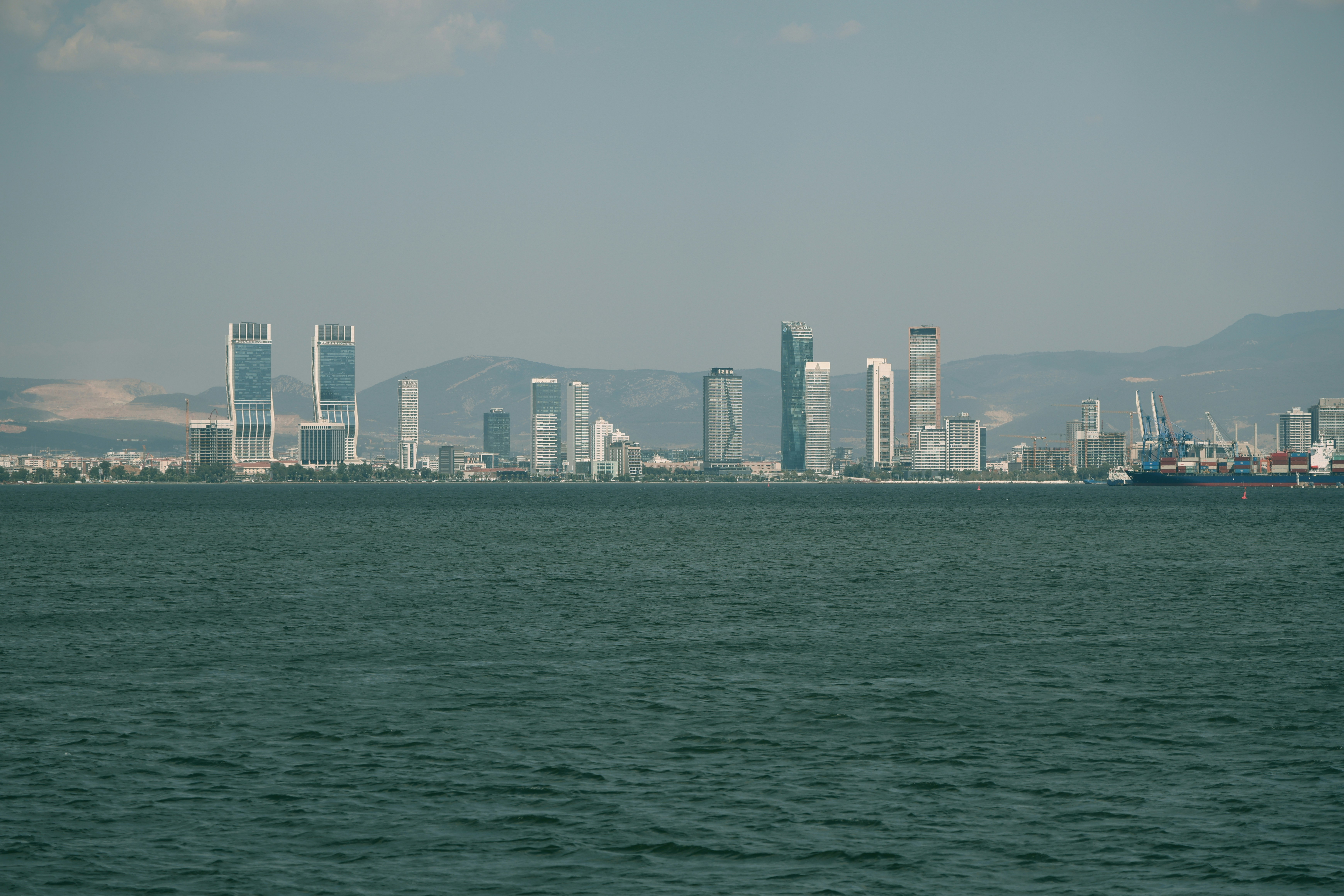 City skyline along a calm sea with distant hills, emphasizing the horizon and architectural silhouettes; a minimal coastal panorama.