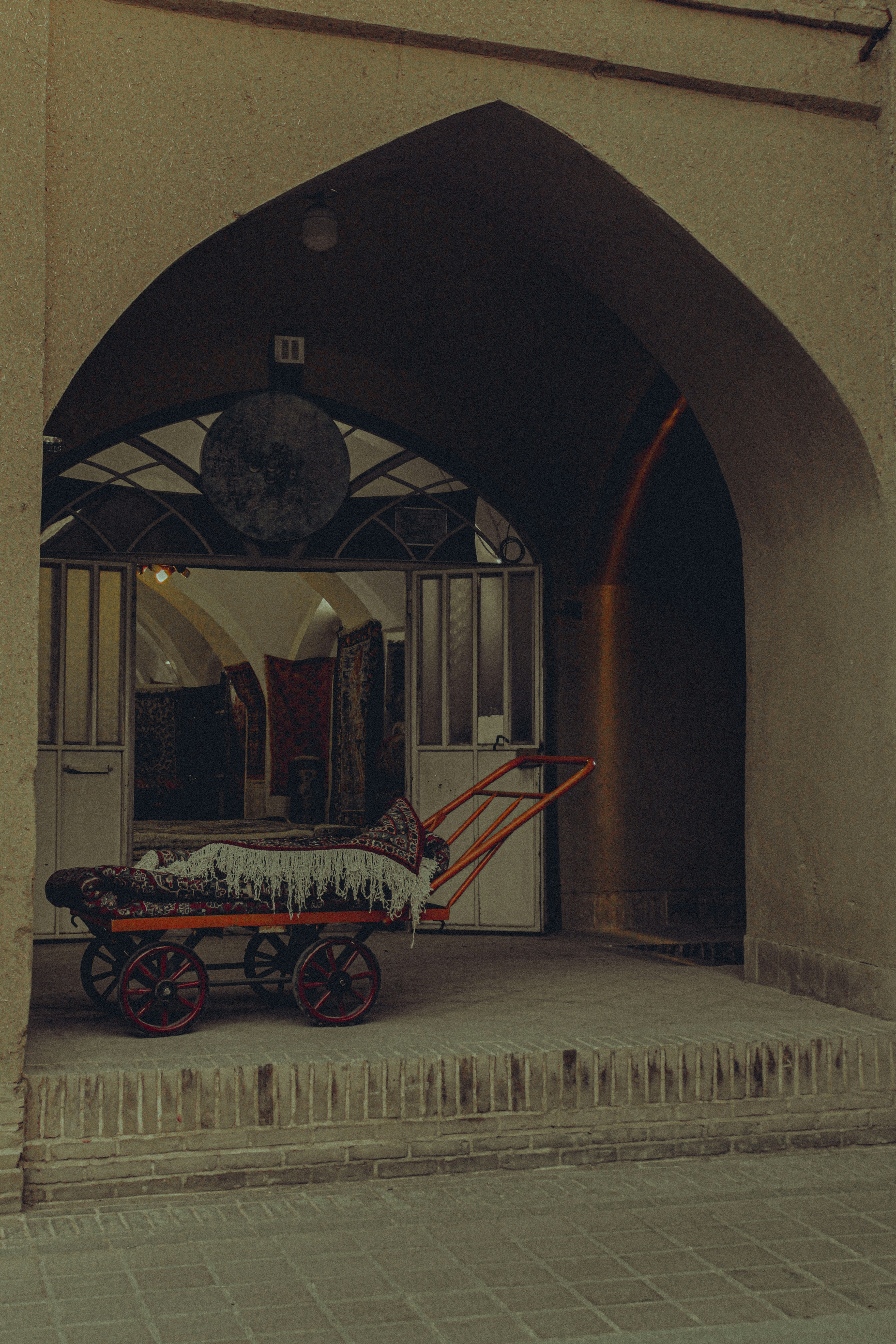 Wheeled red carriage at the archway of a quiet, shadowed doorway