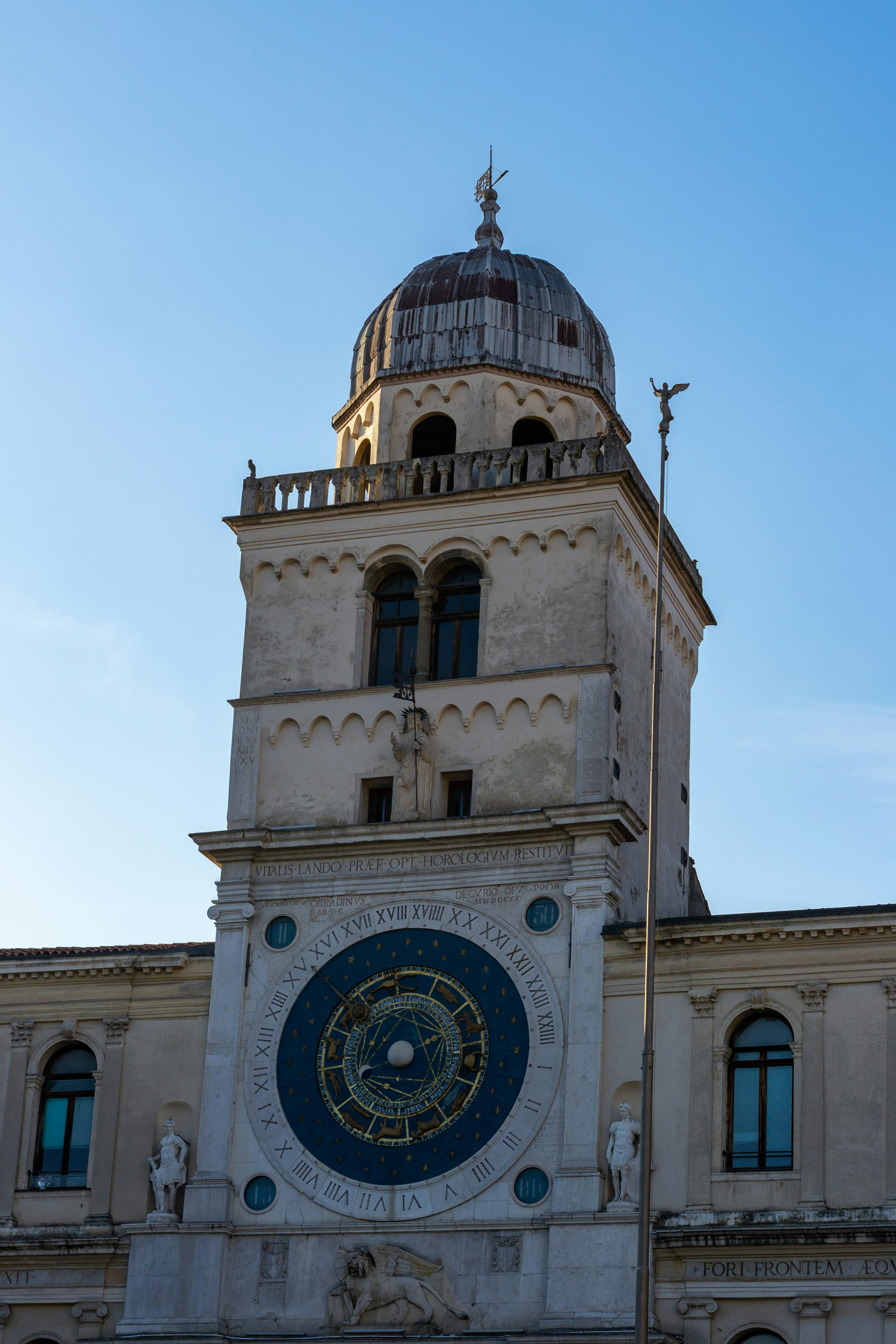 Astronomical clock tower with a domed cupola and ornate facade, set against a clear blue sky.