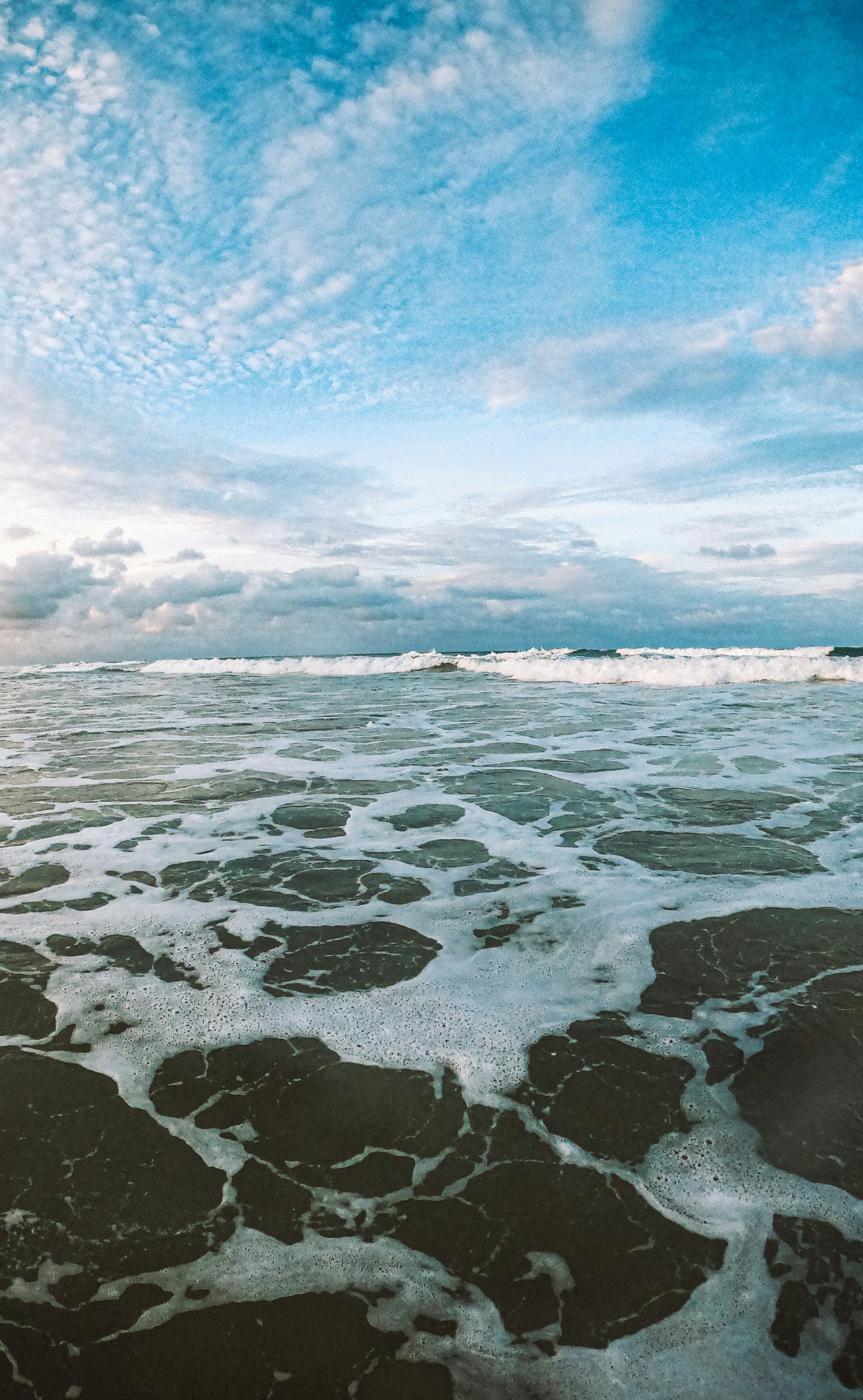 Foamy shoreline mirror: ocean at the horizon under a bright sky