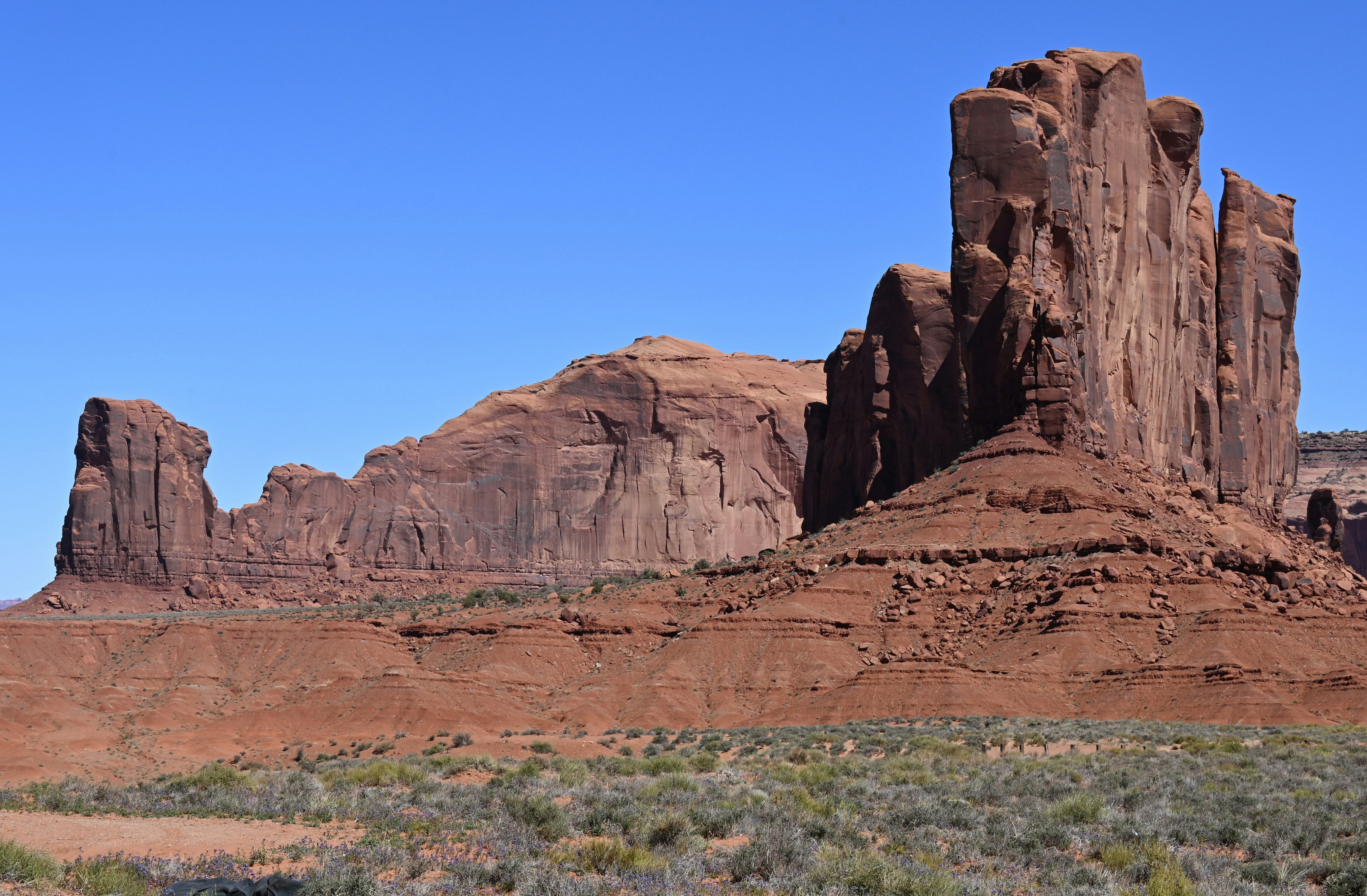 Jagged red rock formations rise from a barren desert plain under a crisp blue sky.
