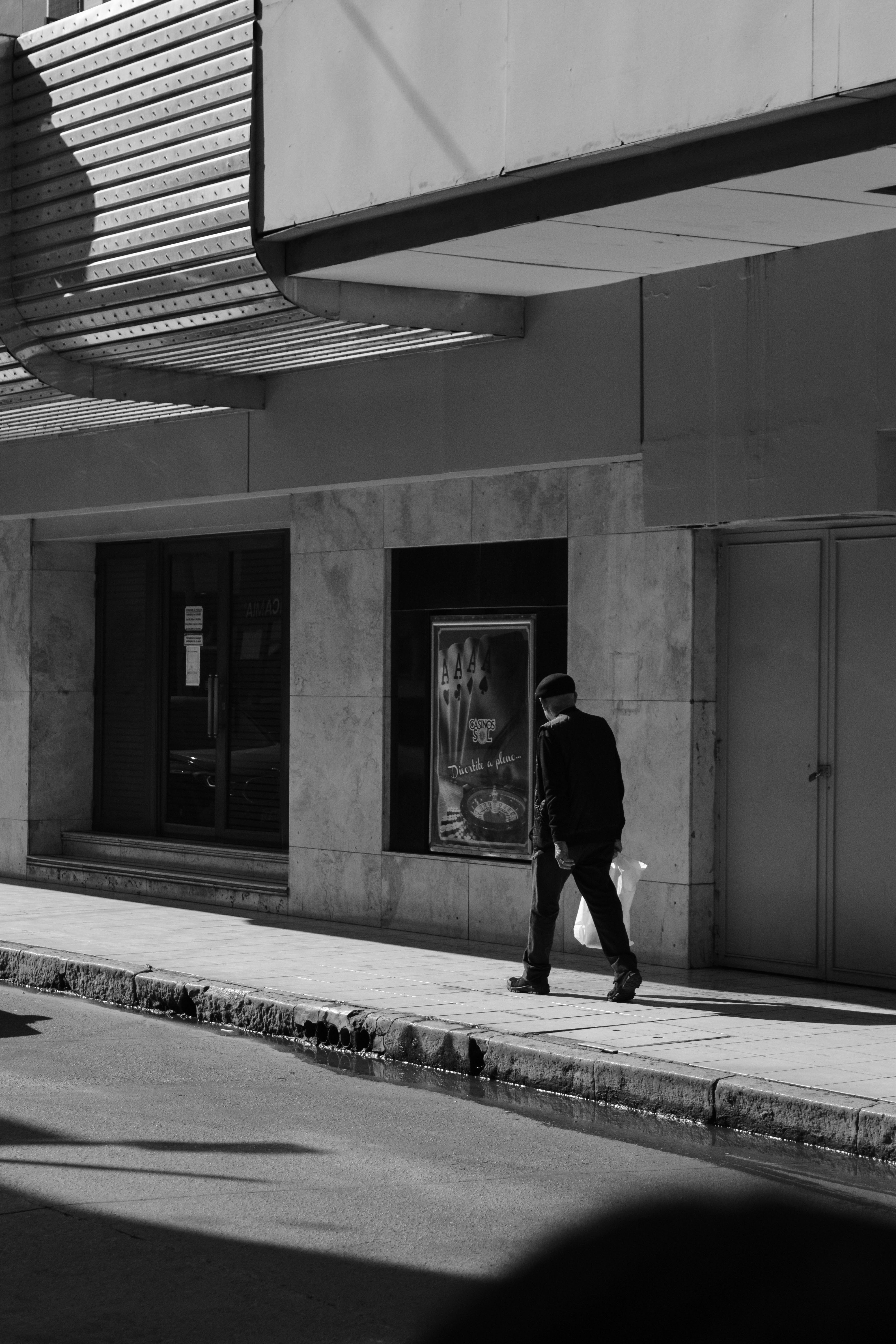 Footsteps in Shadow: A solitary figure walks the storefront street
