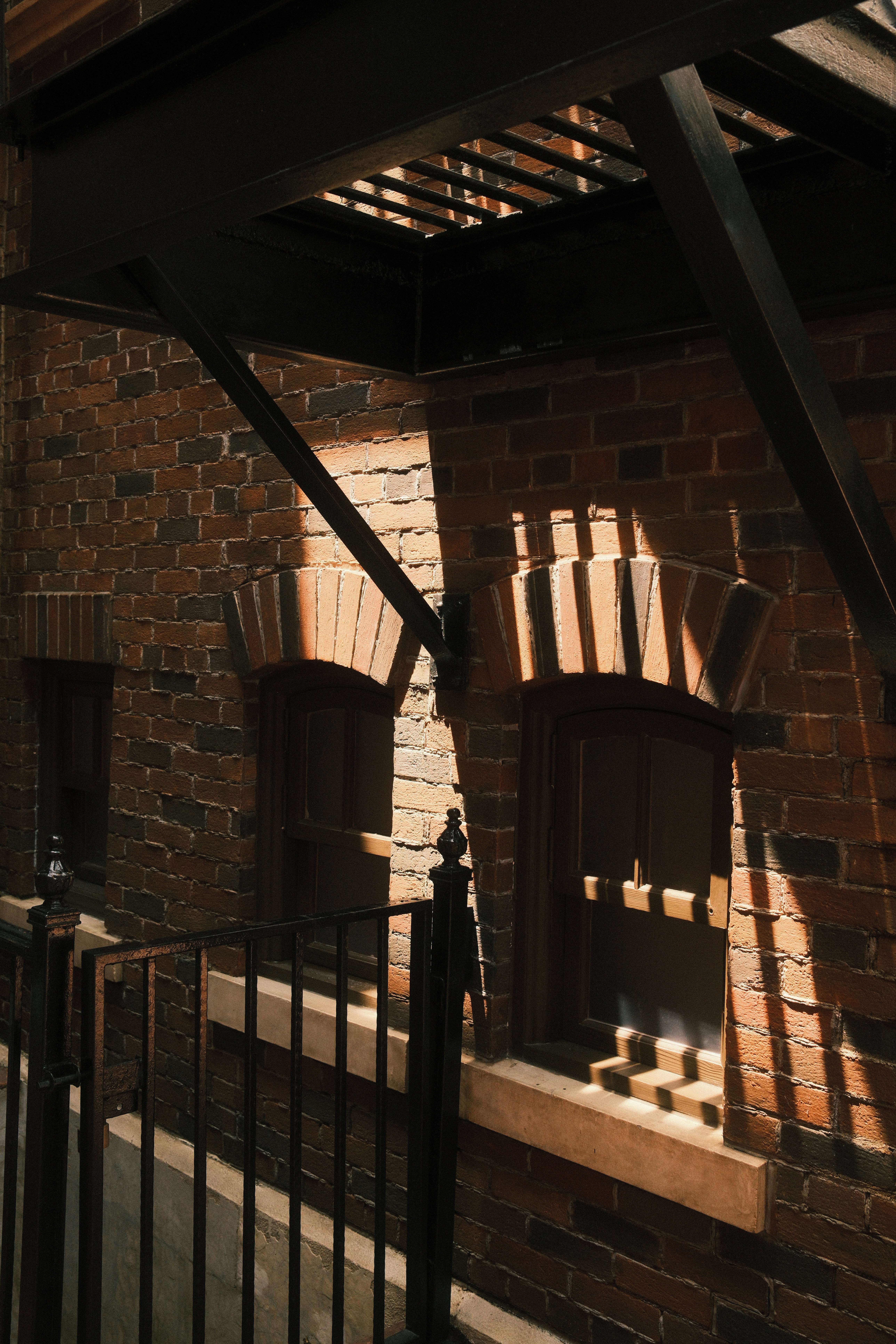 Sunlit Brick Stairwell: Ironwork Shadows in a Quiet Courtyard