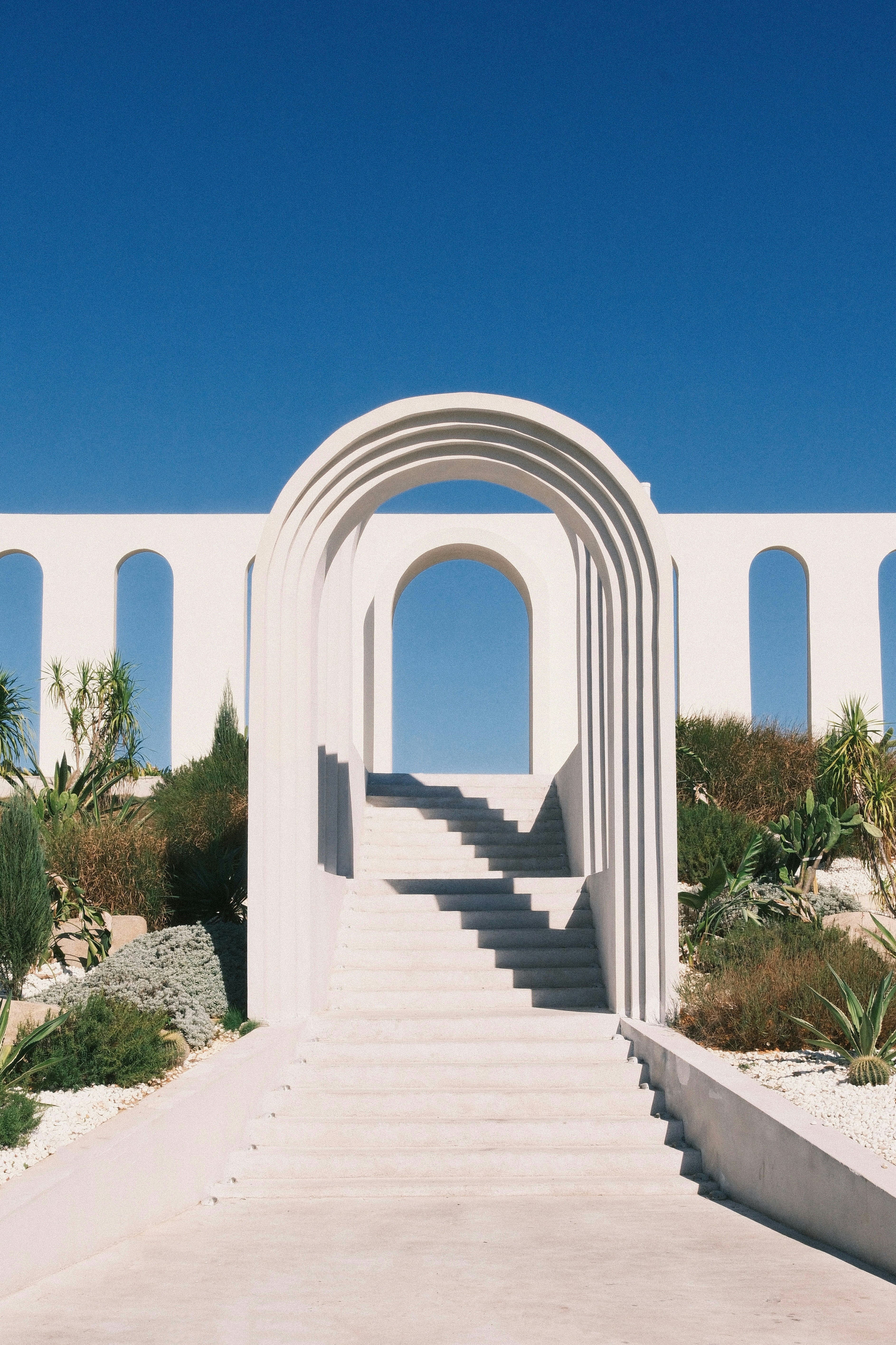 Arched Ascent: White Staircase Through a Concrete Garden