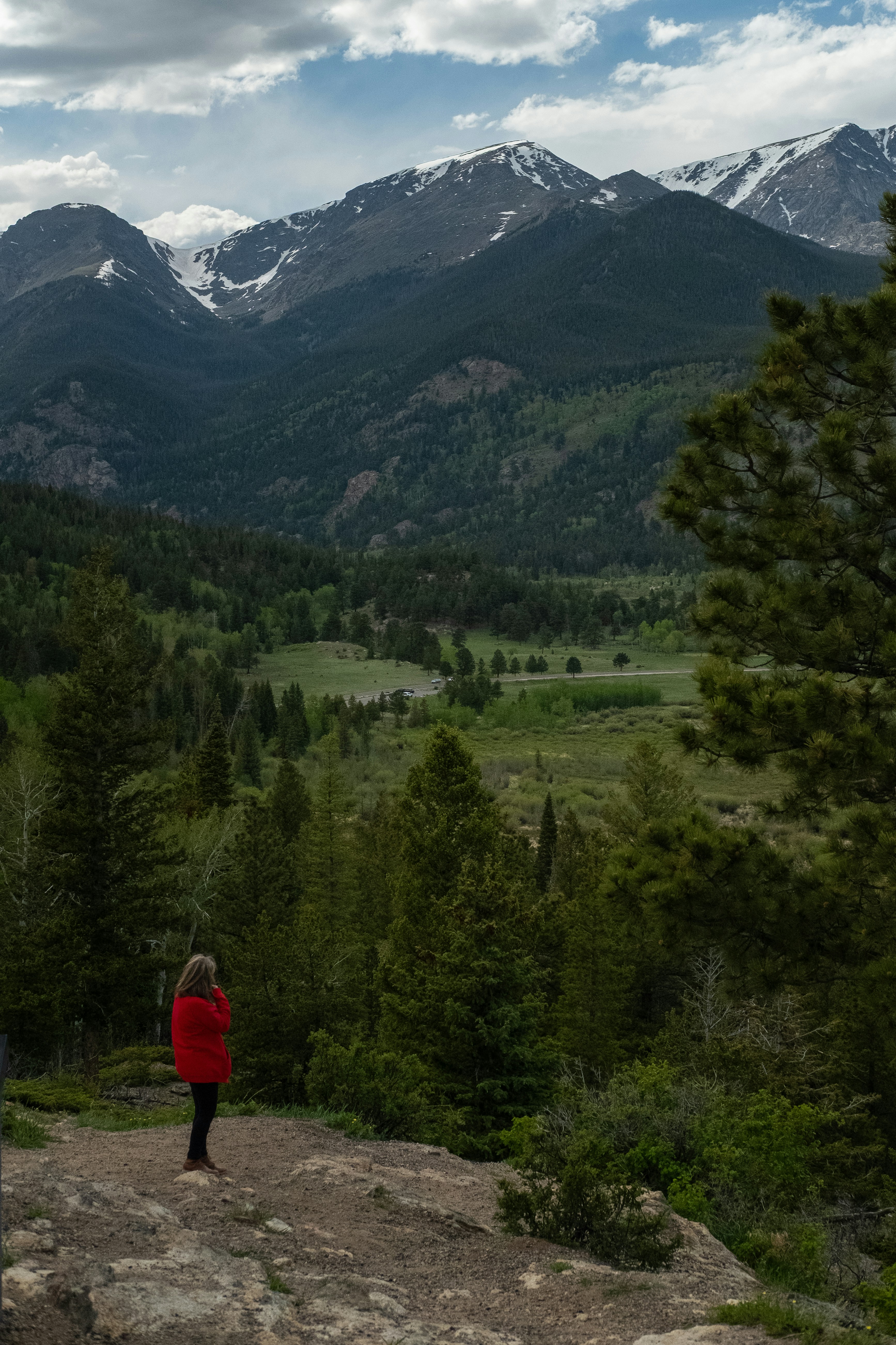 Red-clad observer on a rugged overlook beneath snow-dusted peaks
