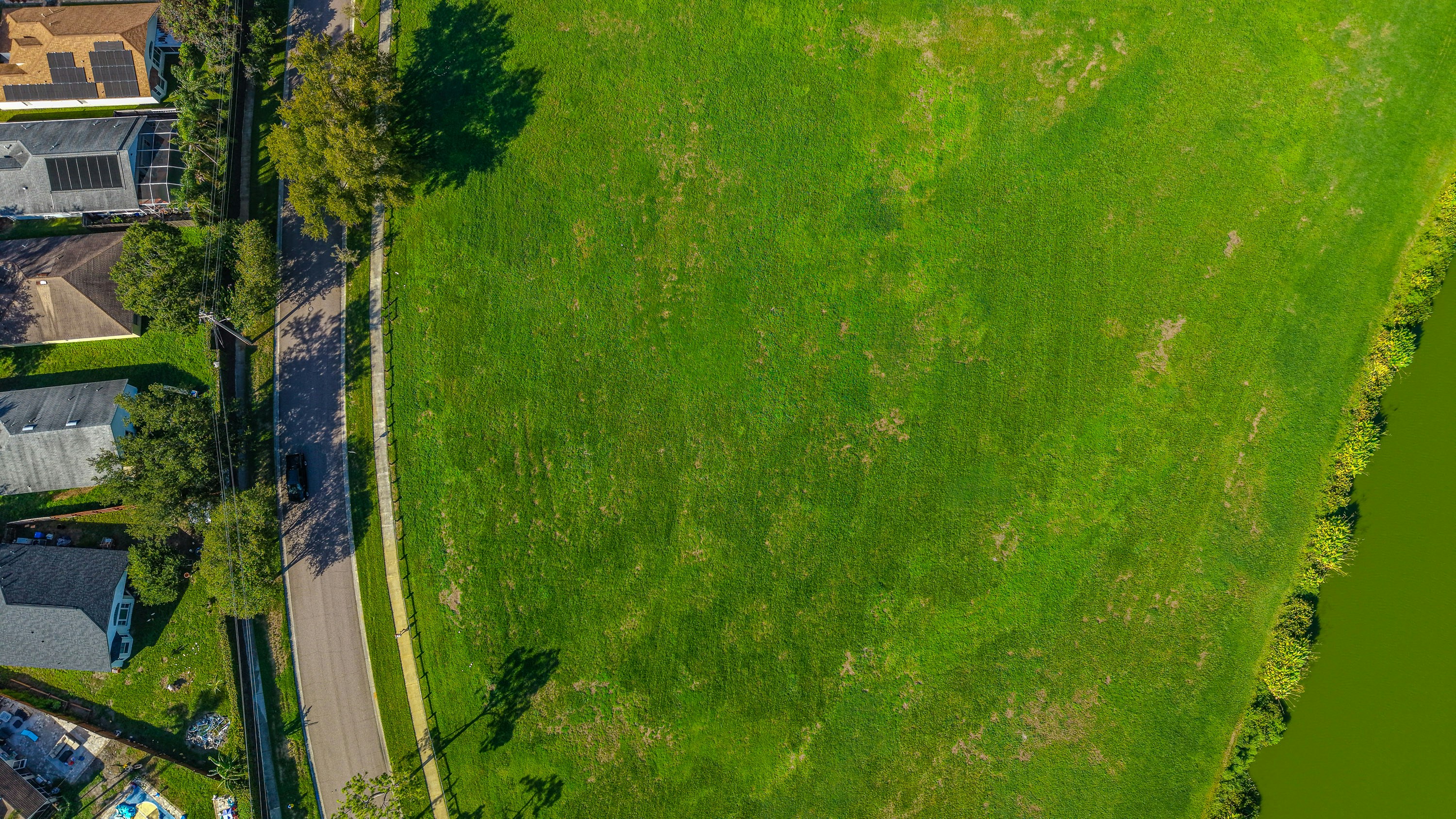 Aerial View of Green Field Bordering a Quiet Suburban Road