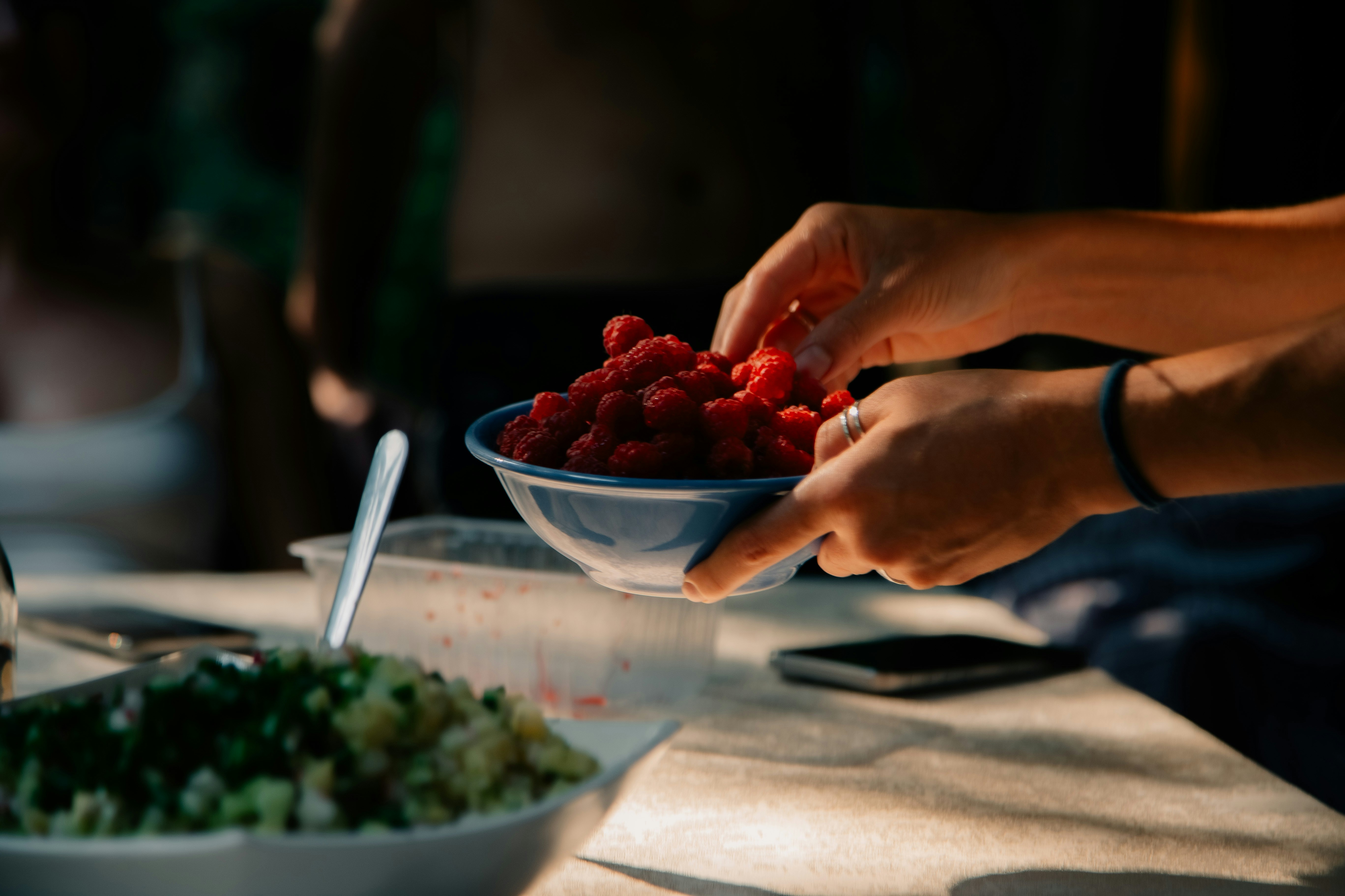 Hands Lift a Bowl of Raspberries Over a Dinner Table Sketch