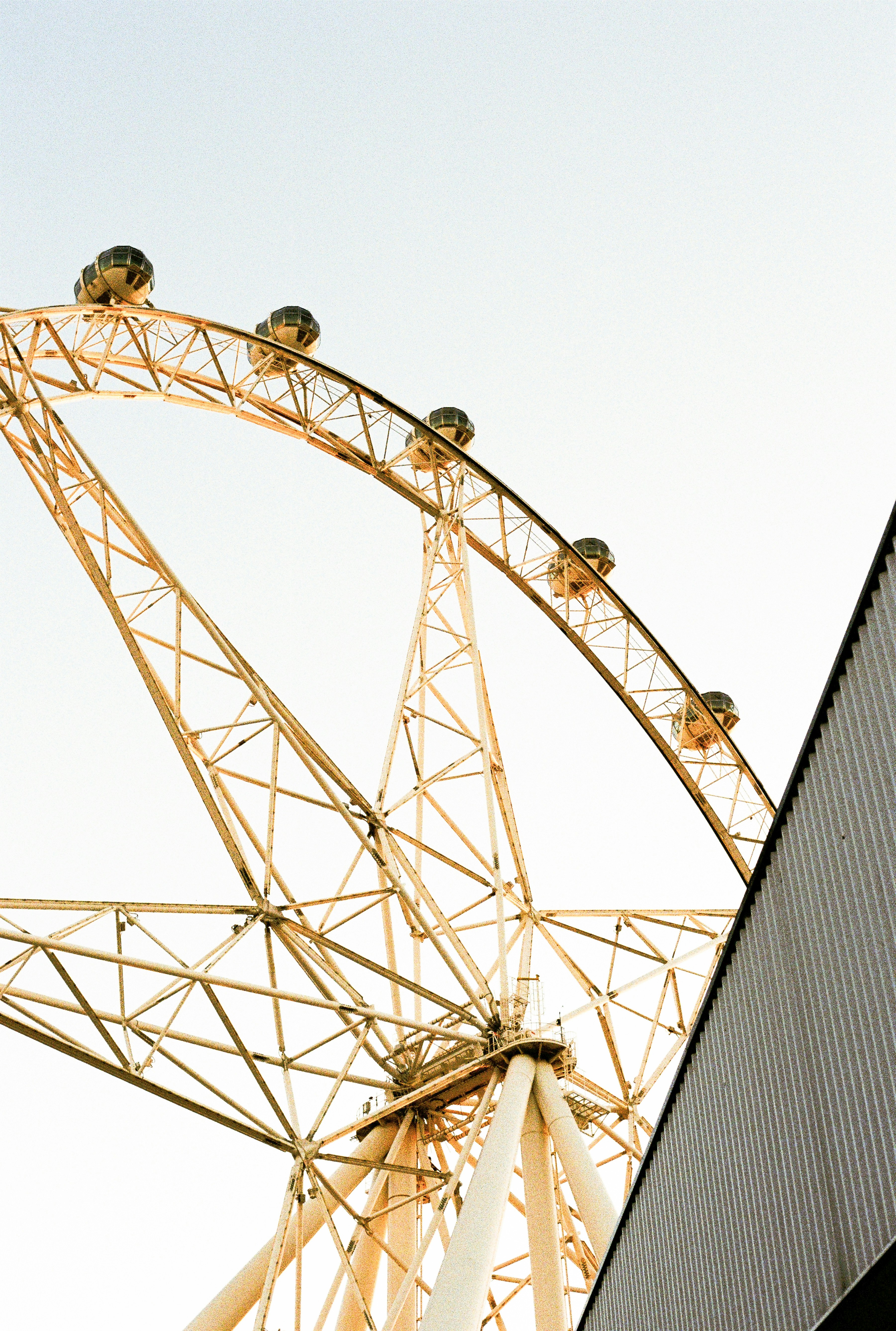 Light-filled ferris wheel lattice against a pale sky, with a sharp diagonal roof edge in the foreground.