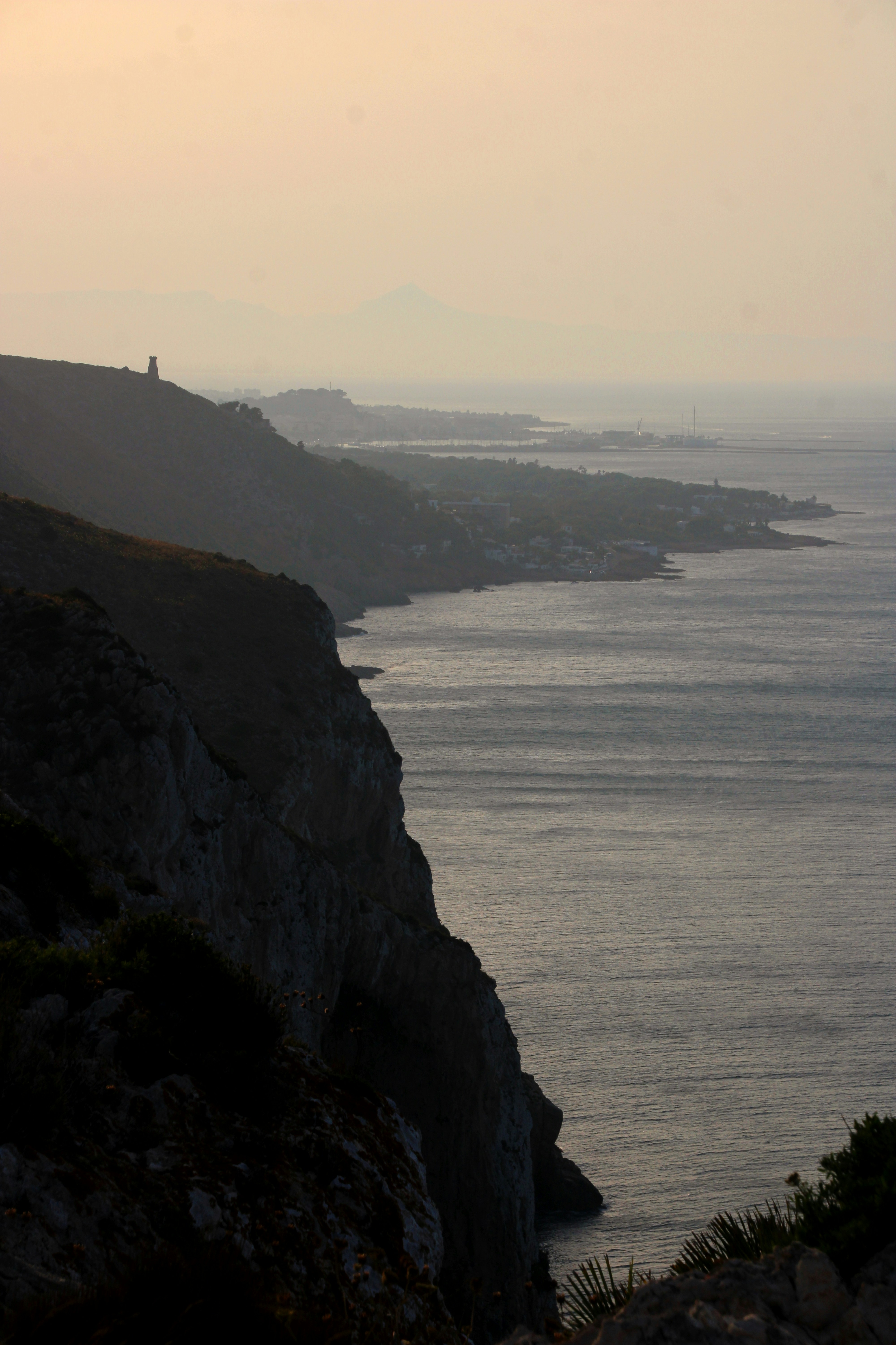 Distant Lighthouse Silhouette Over Quiet Coastal Cliffs at Sunset