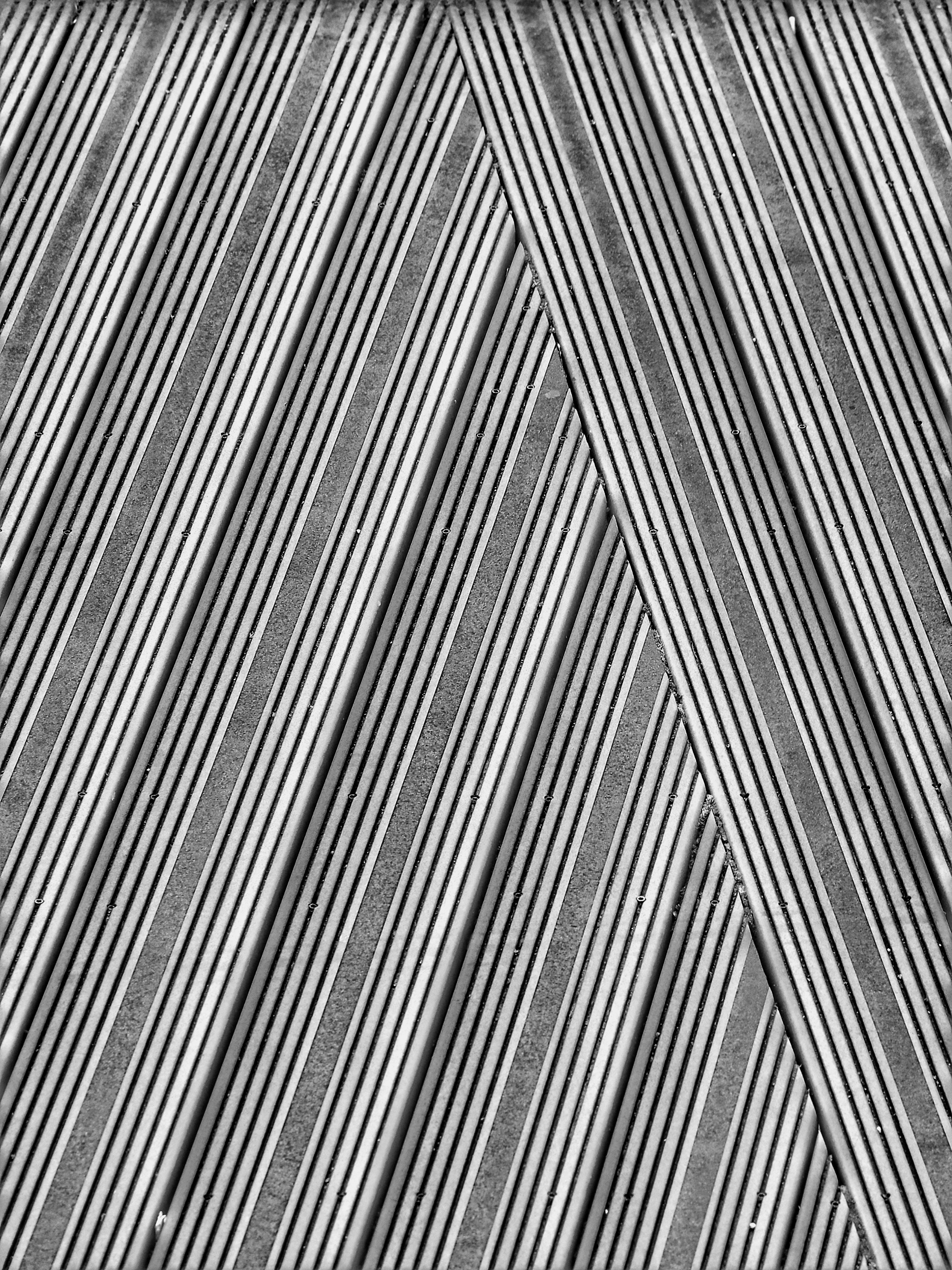 Monochrome geometric pattern of diagonal lines intersecting in V-shaped forms, creating depth and rhythm across the frame. Abstract architectural texture highlight.