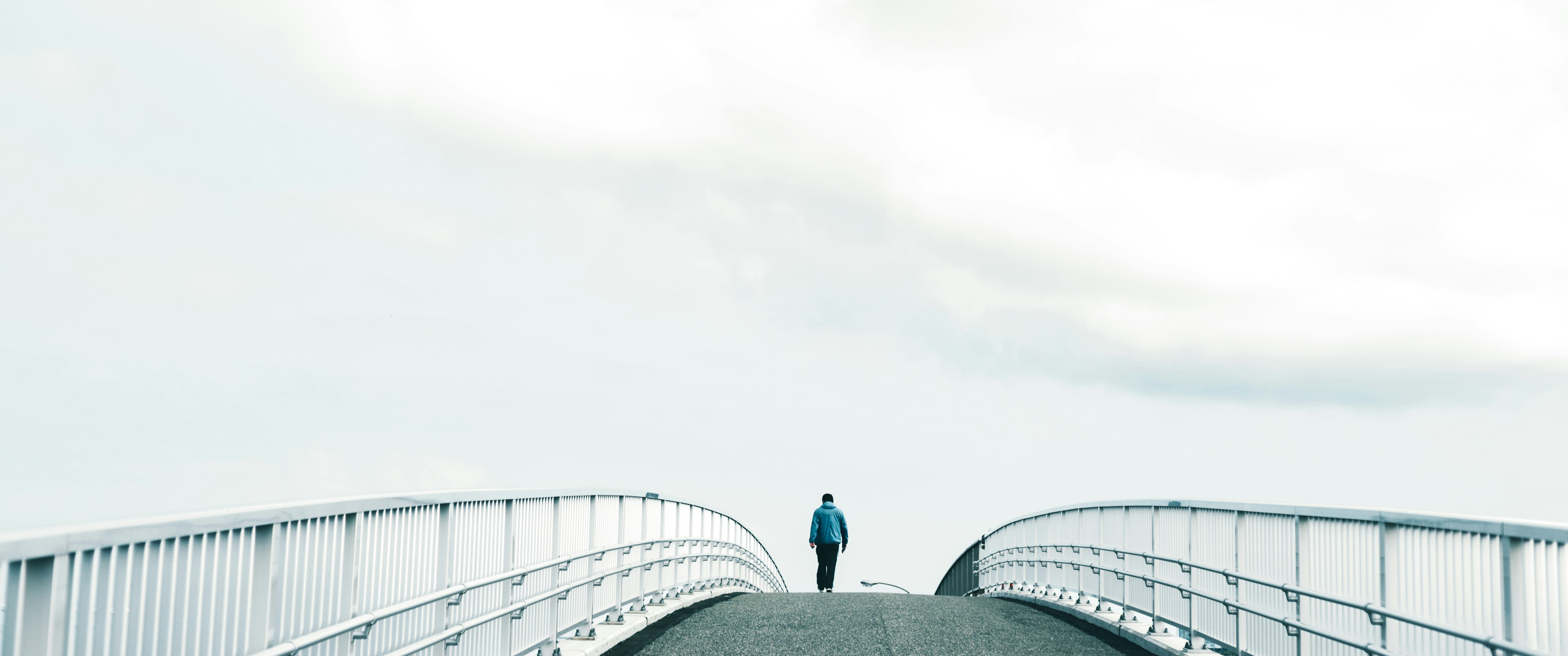 A lone wanderer on a misty bridge toward the horizon